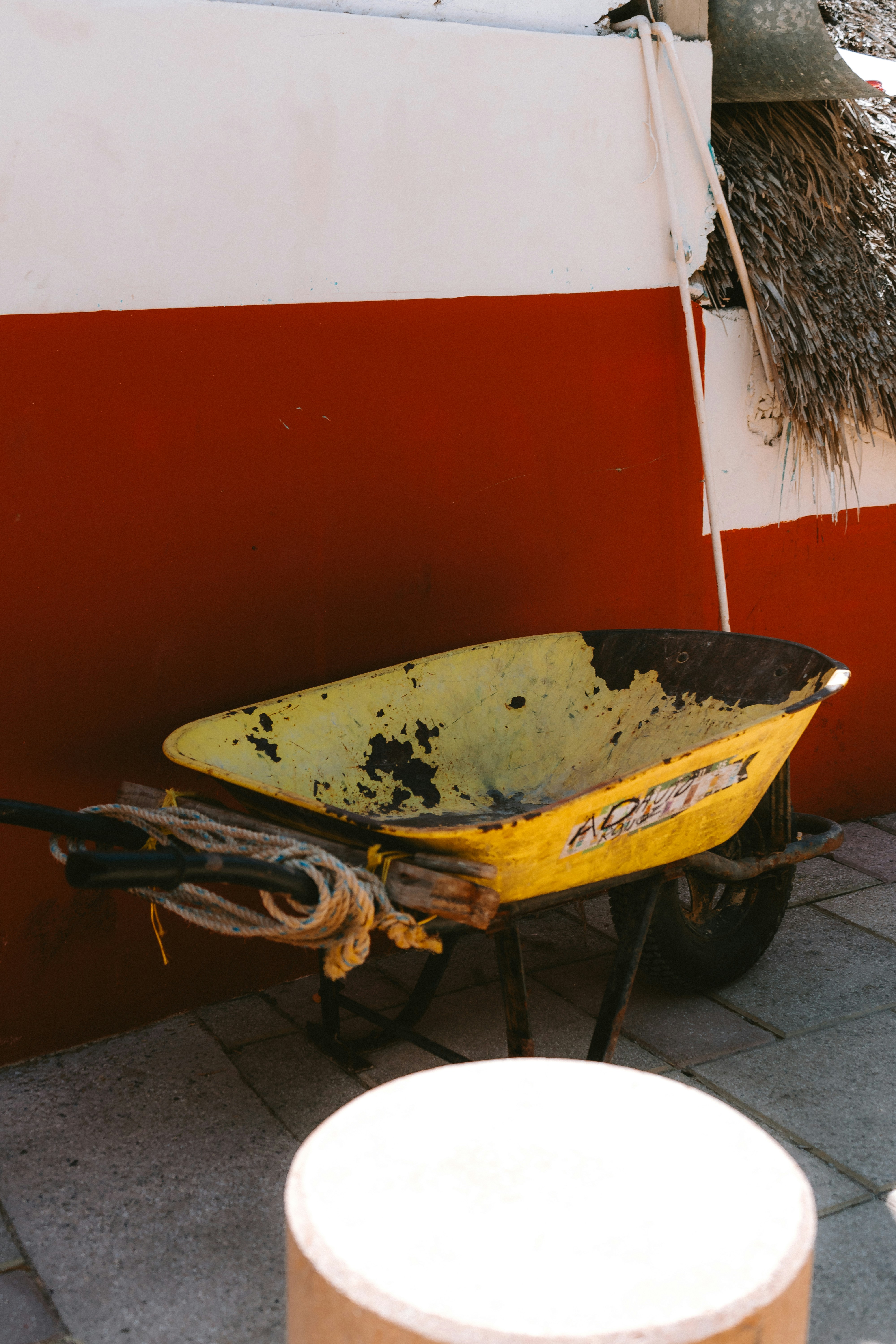 Weathered Yellow Wheelbarrow Resting Against a Crimson-White Facade