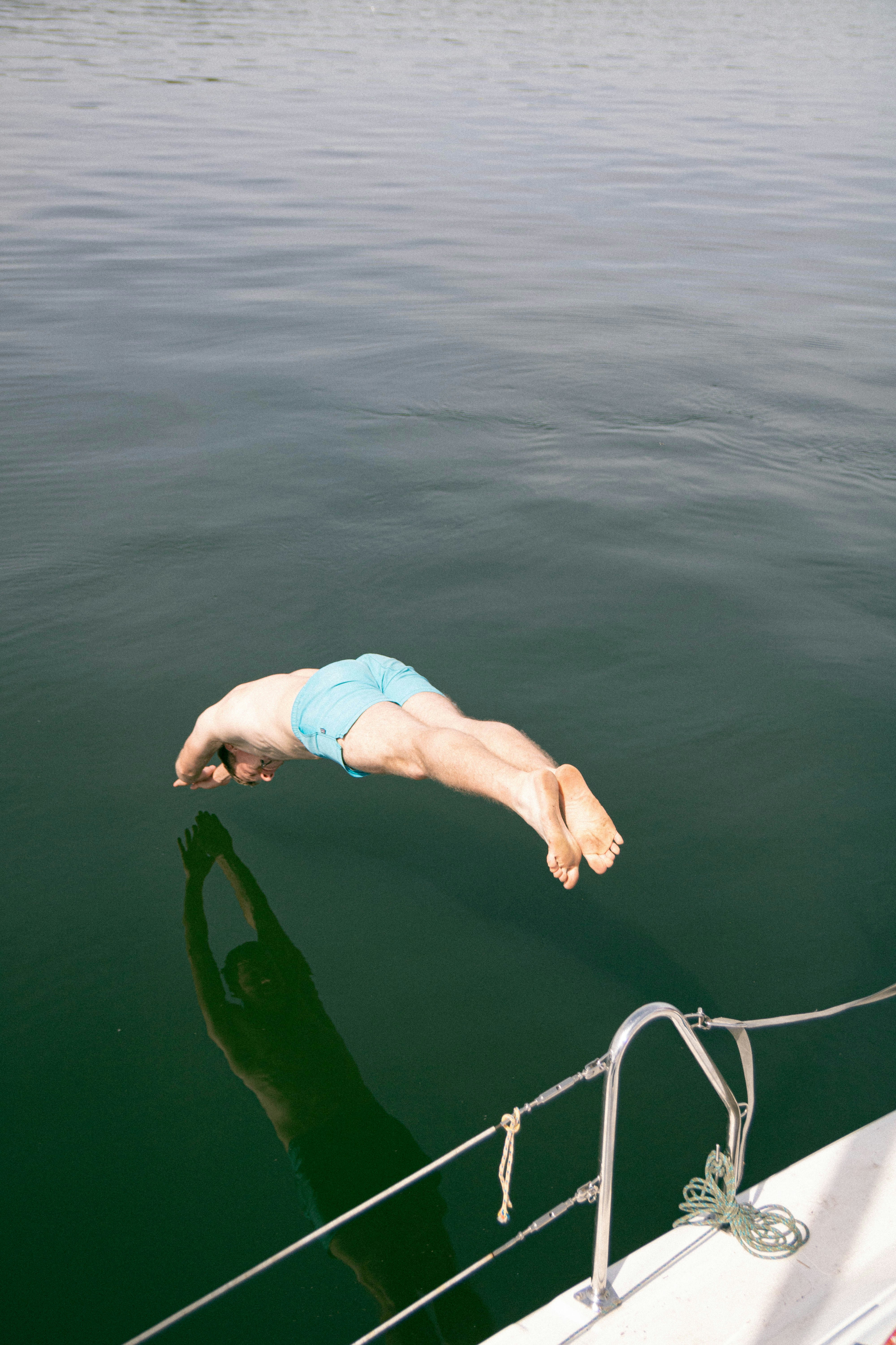 Emerald Wake Leap: A Diver Arcs Off a Sailboat Into Green Water