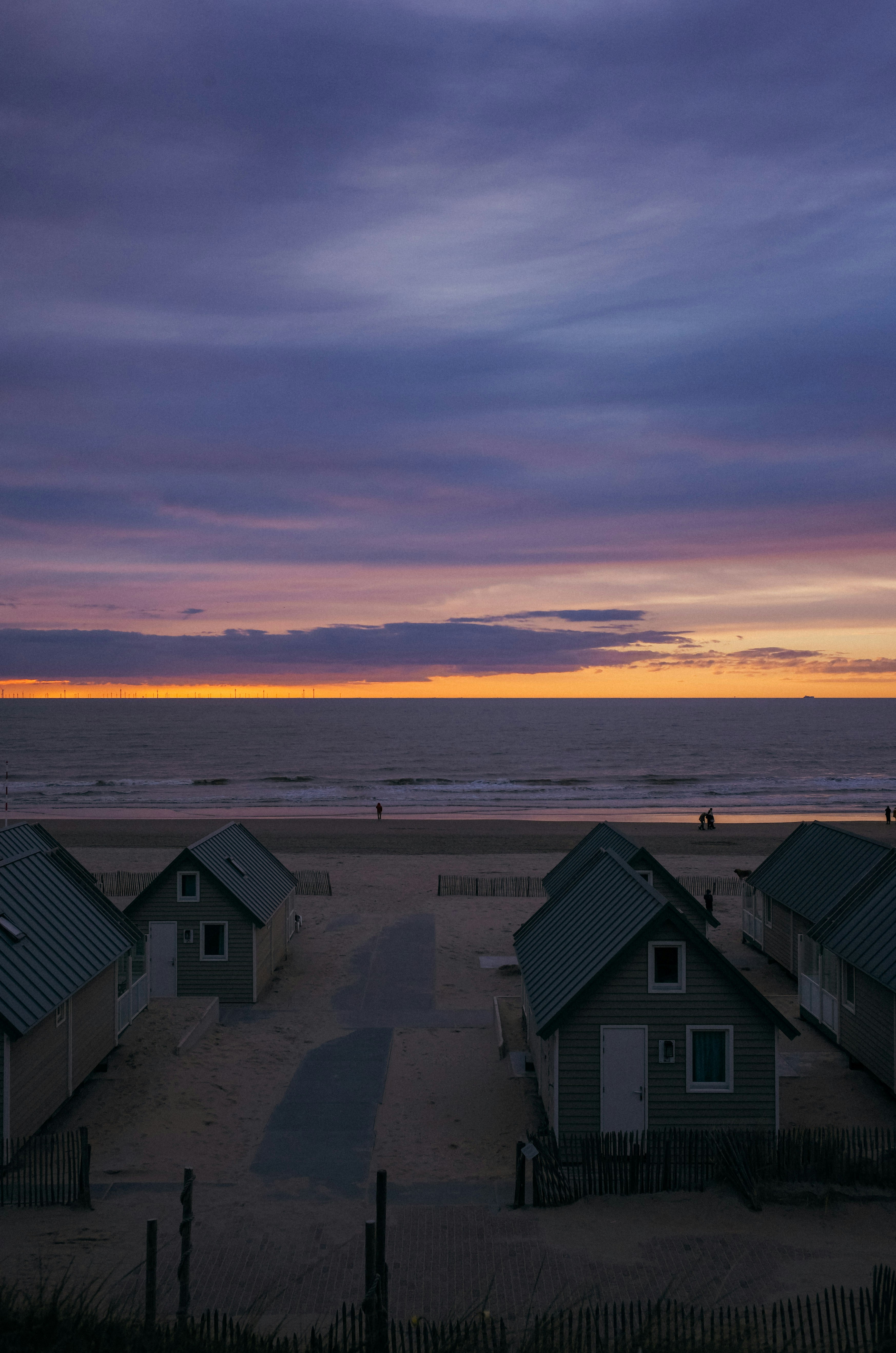 Wooden cabins on a sandy beach with a vibrant sunset sky over the ocean.
