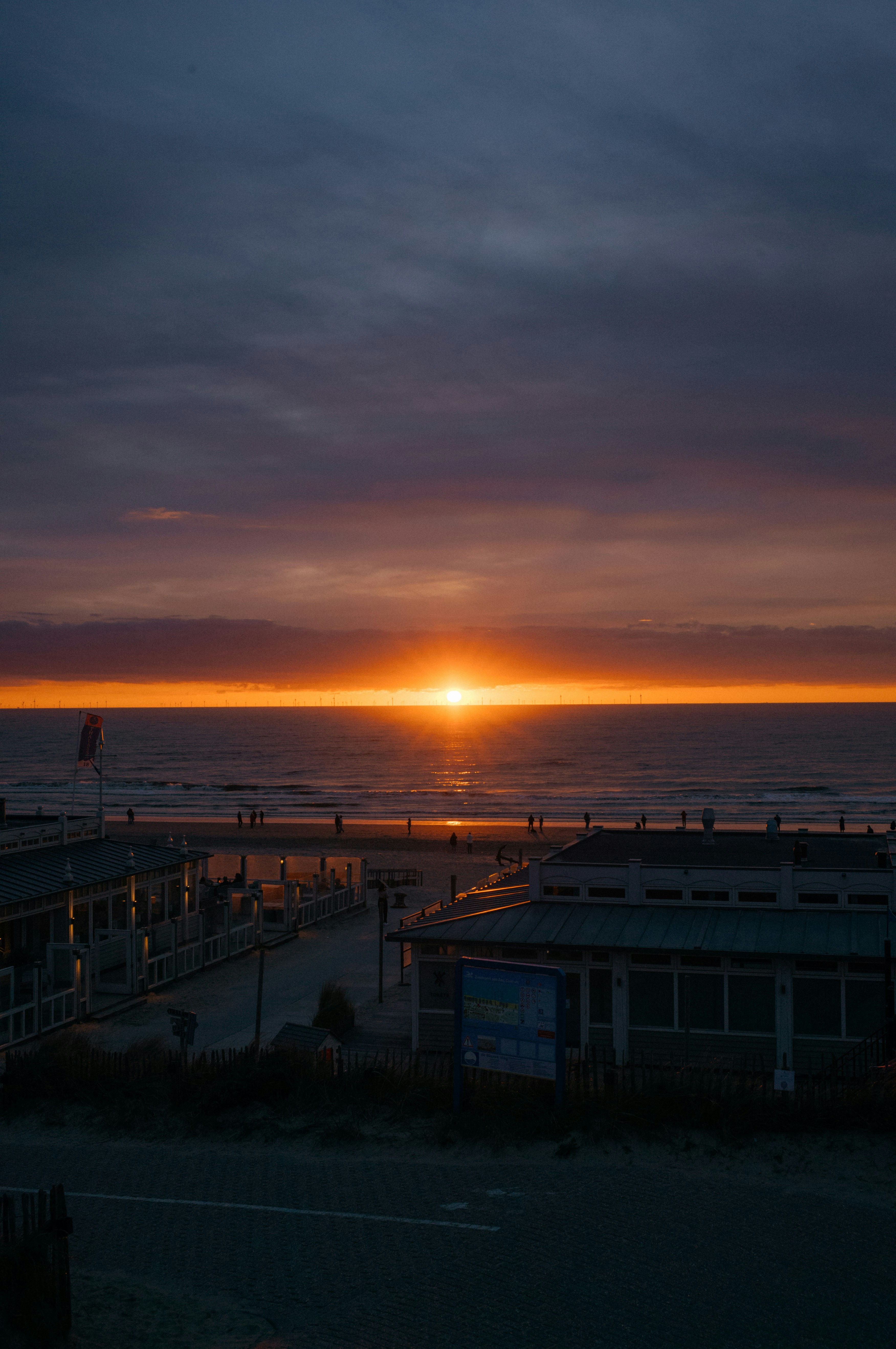 Sunset casting vibrant hues over a calm ocean with silhouetted buildings in the foreground.