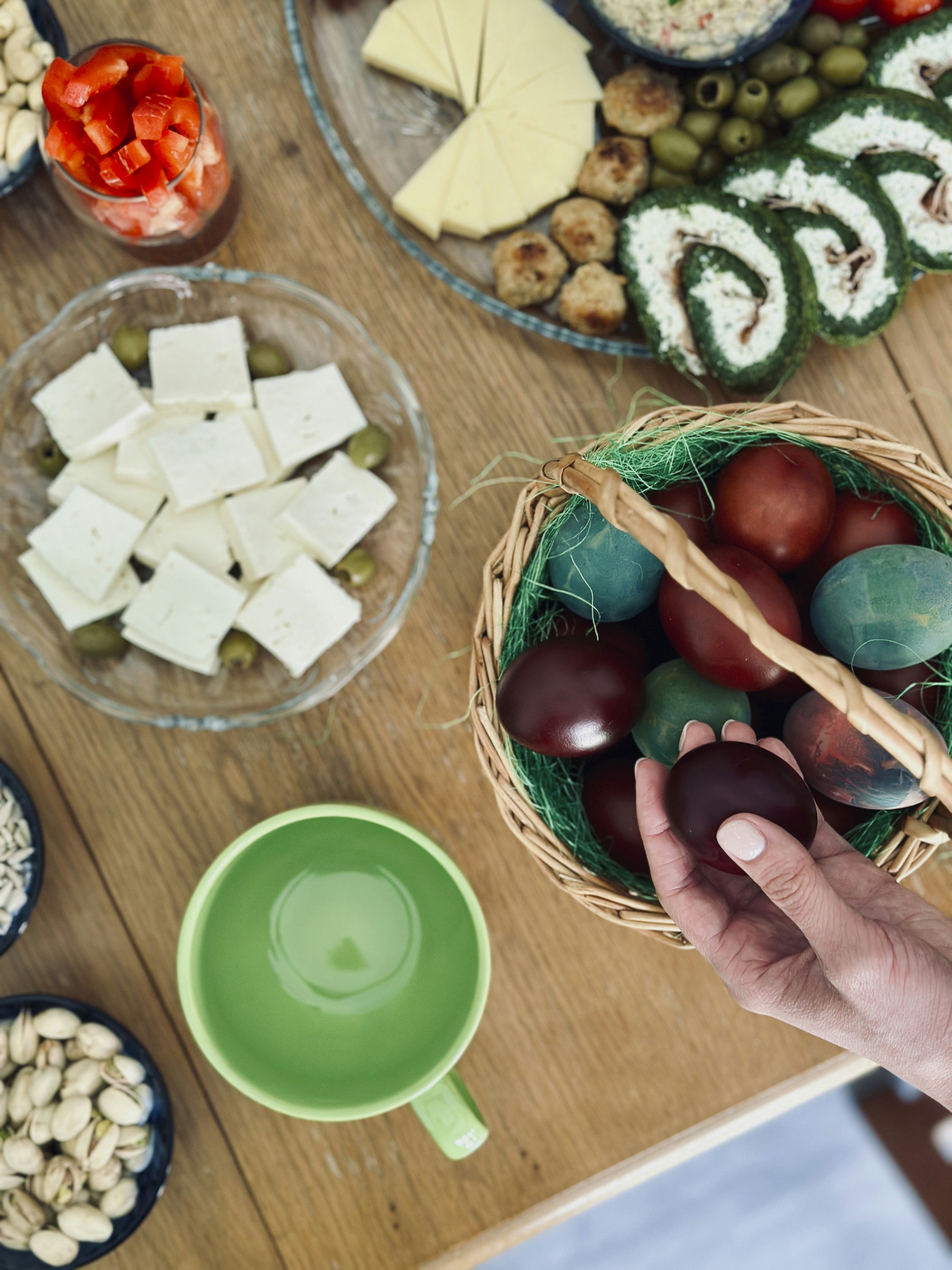 Hand Reaches for Jewel-Toned Easter Eggs Across a Rustic Table Spread