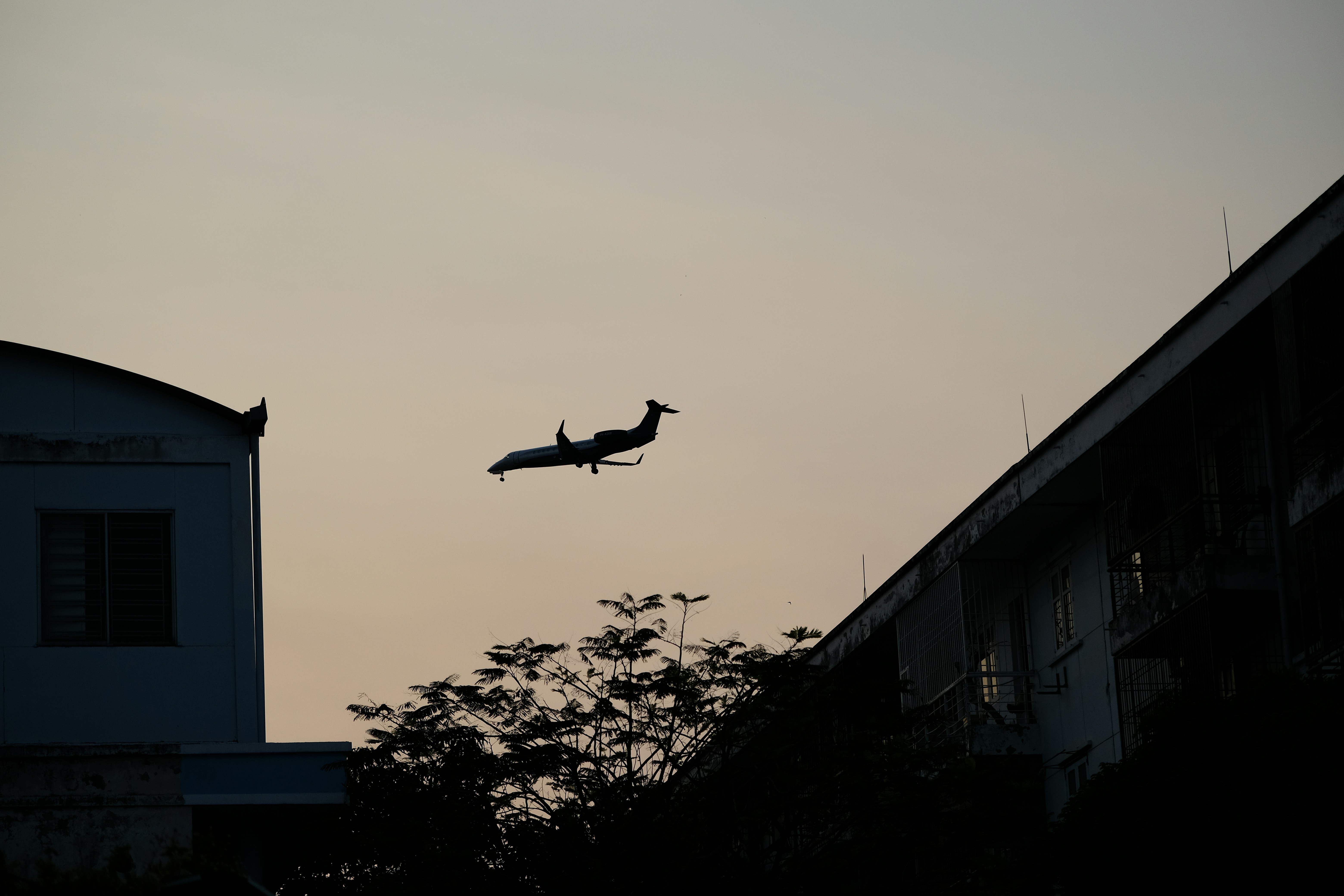 Silhouette Landing: A Jet Descends Between Rooftops at Dusk