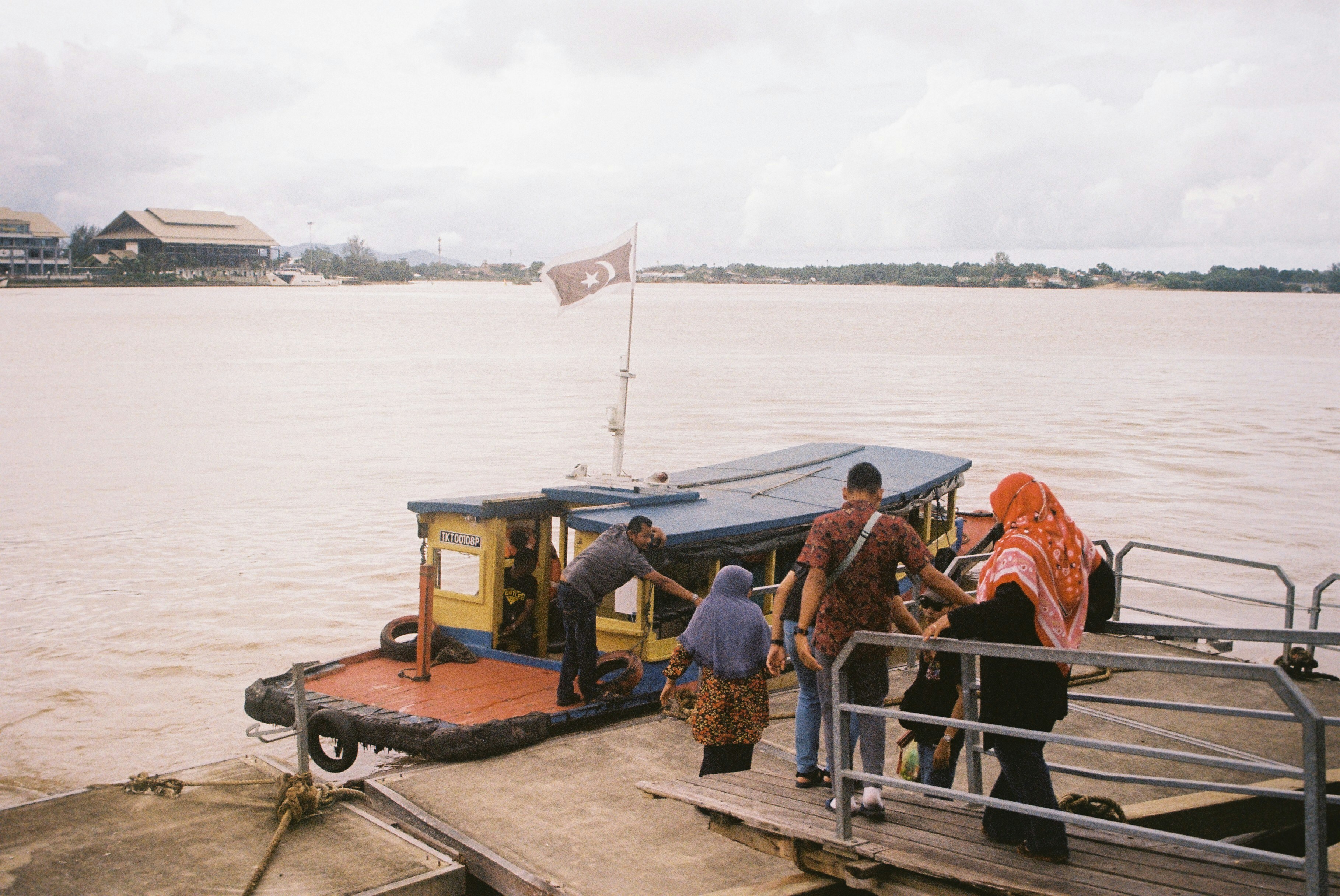 People boarding a small boat at a dock on a cloudy day with calm waters.
