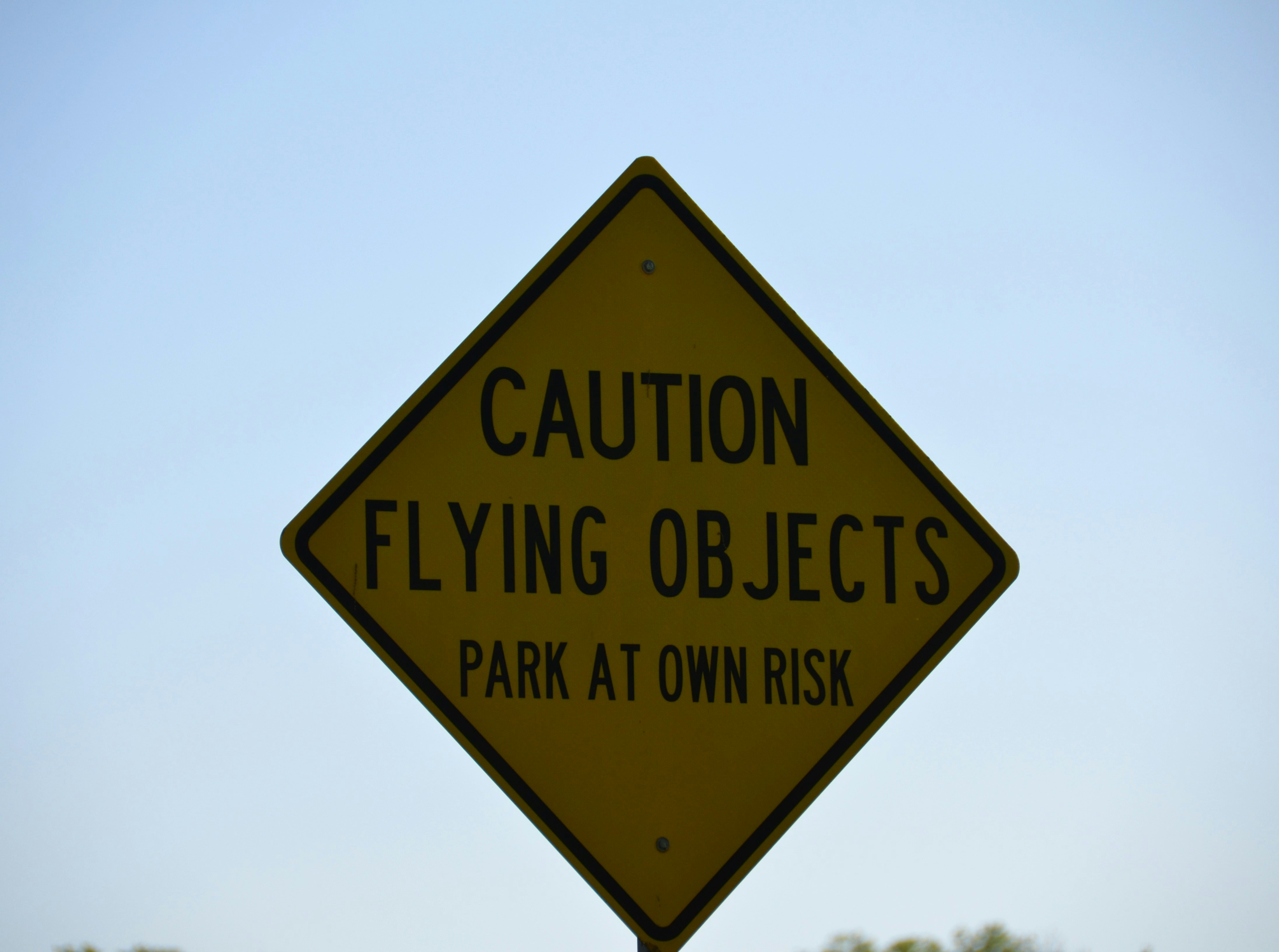 A yellow caution flying objects sign on a pole photo – Free Green Image ...