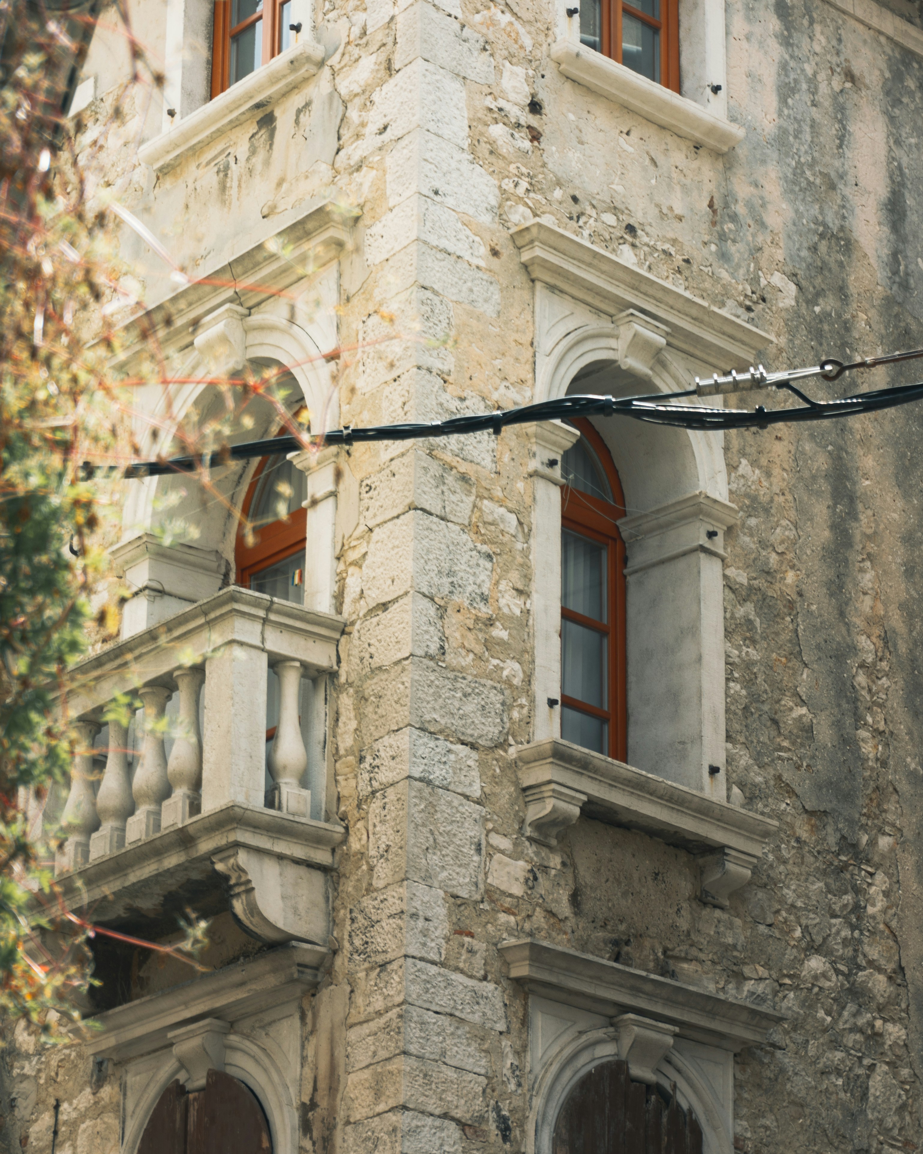 Cracked Stone Manor: Red Window Framed by a Weathered Facade and a Crossing Wire