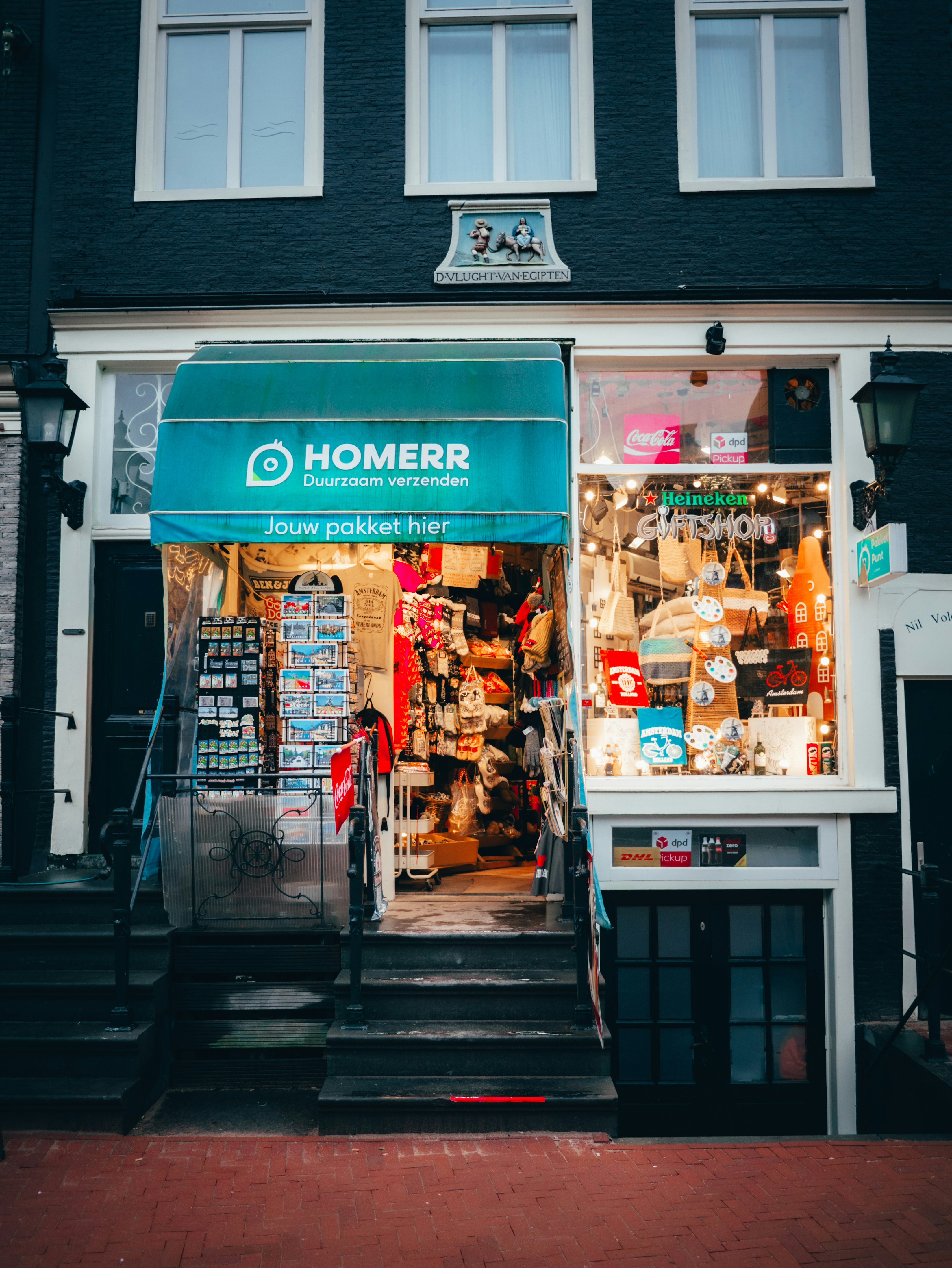Storefront with a teal awning and open doorway, a Dutch parcel shop spilling merchandise and signage into the street.