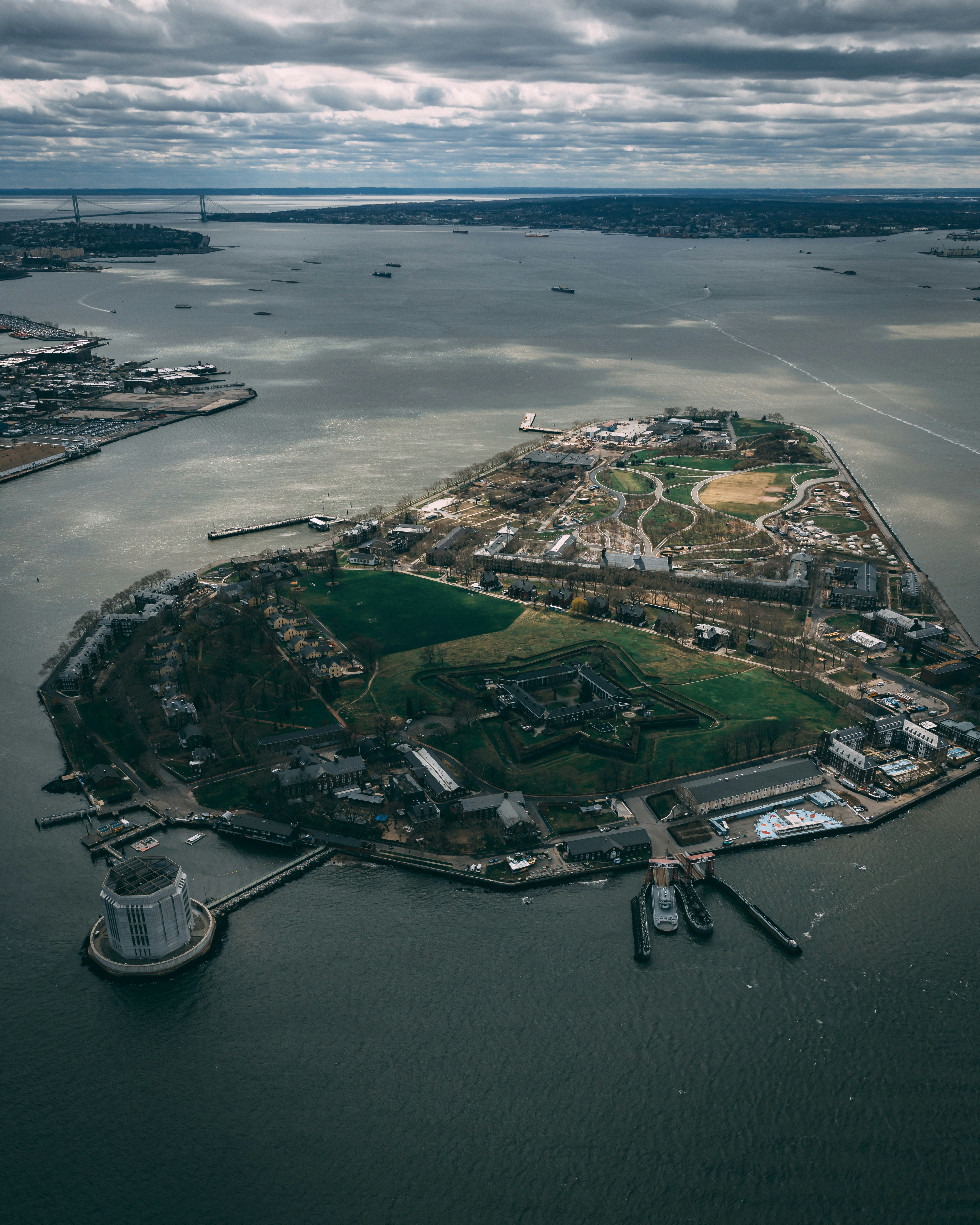 Aerial view of a lush green island surrounded by calm waters, showcasing historical structures and recreational spaces. The scene captures the tranquil essence of the landscape.