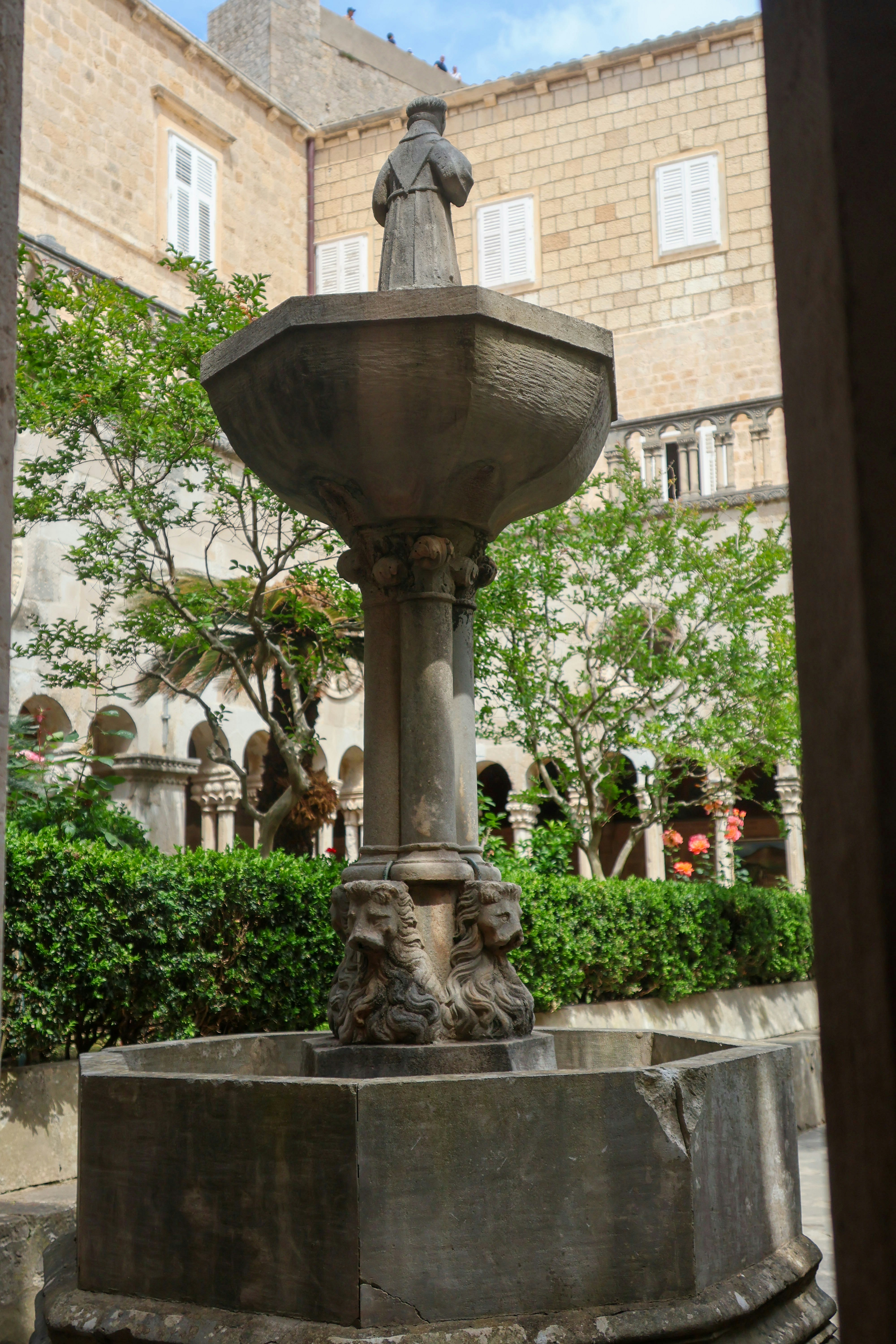 Stone Fountain Crowned by a Statue in a Sunlit Cloister Courtyard