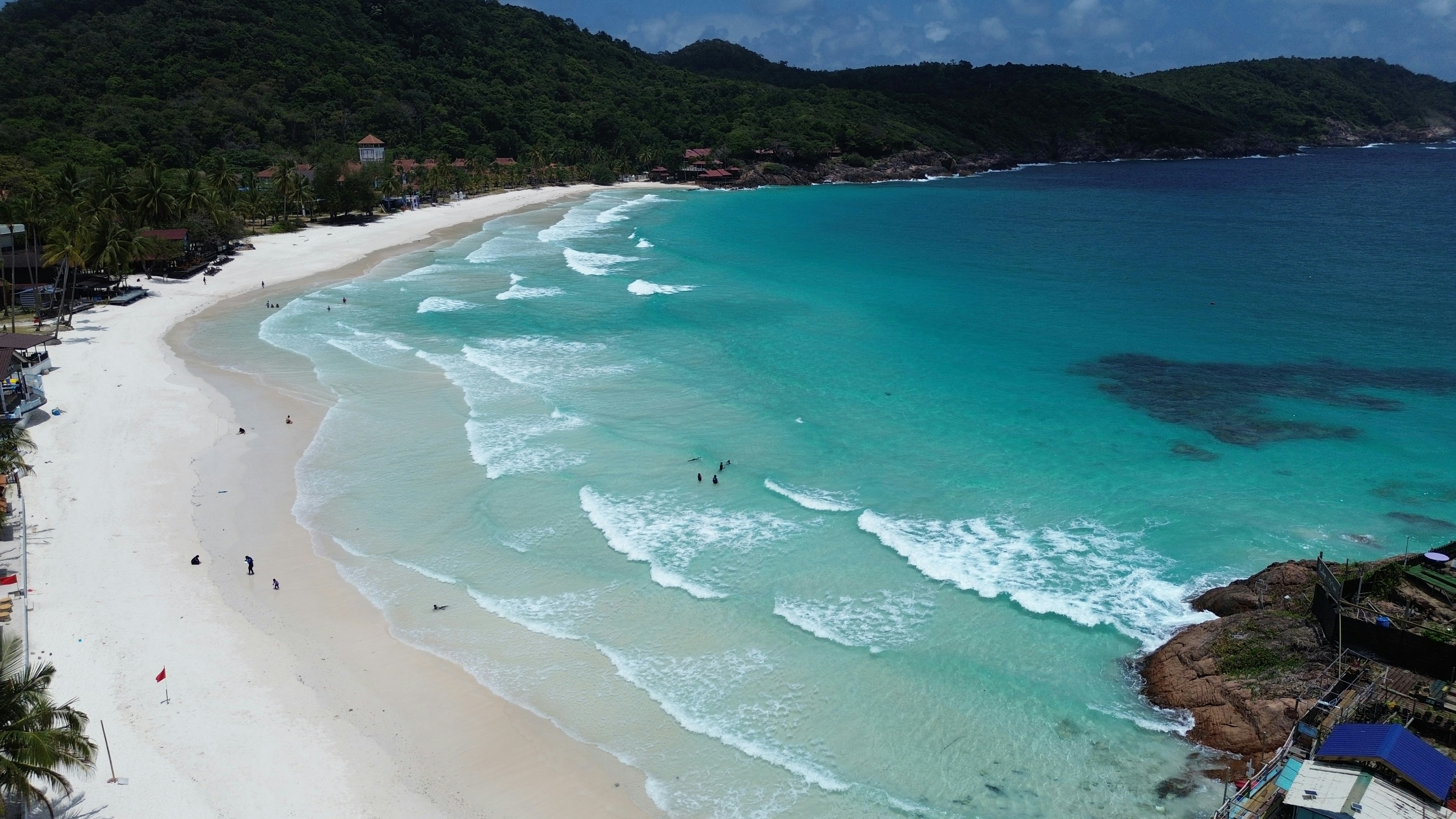 Aerial view of a tranquil beach with gentle waves lapping at the shore, surrounded by lush greenery and rocky formations.