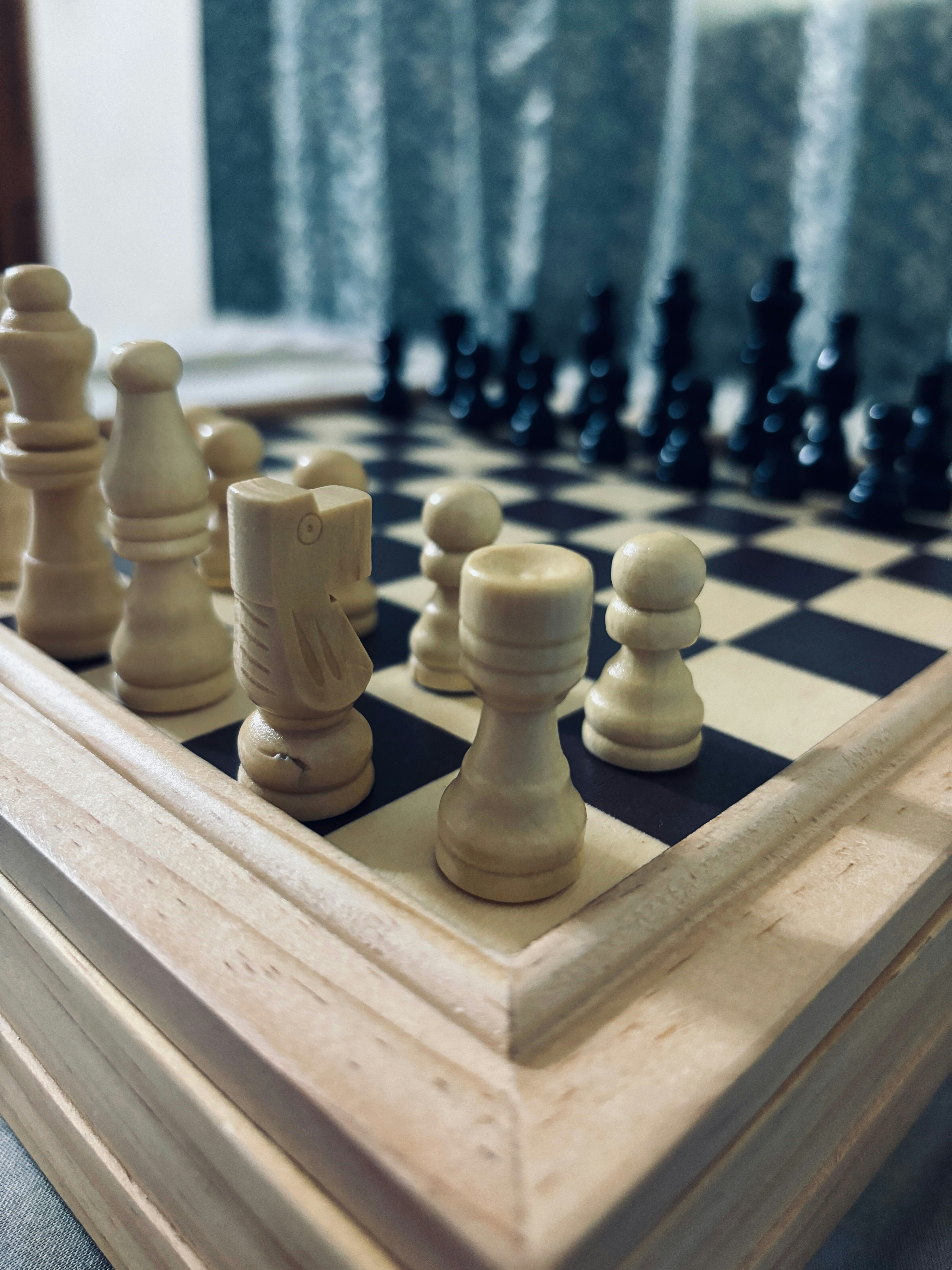 Close-up of a wooden chessboard featuring intricately carved pieces, emphasizing a strategic game in progress. The contrasting colors of the pieces create a dynamic visual narrative.