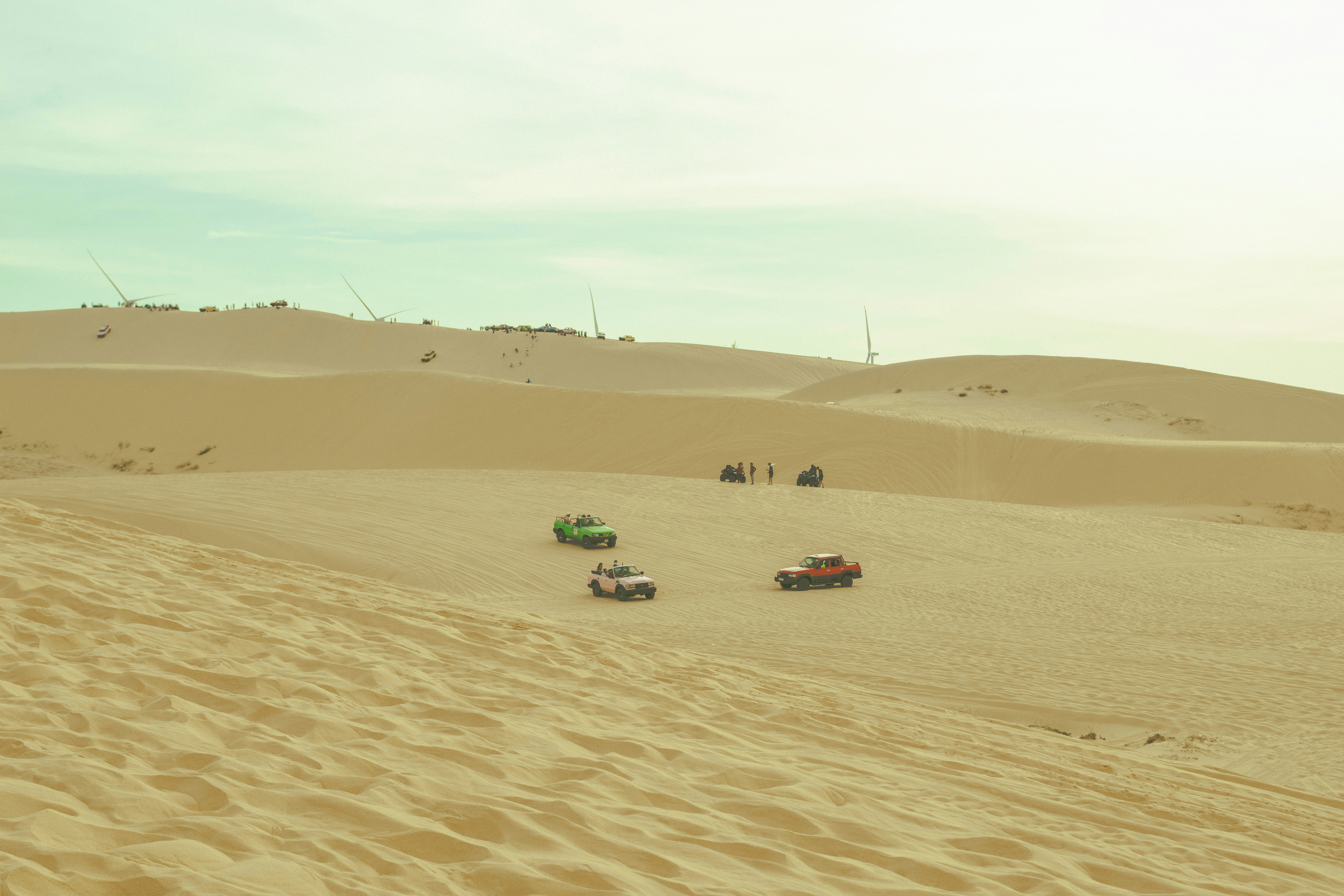 Miniature Rally Across Golden Dunes Beneath a Wind-Turbine Horizon