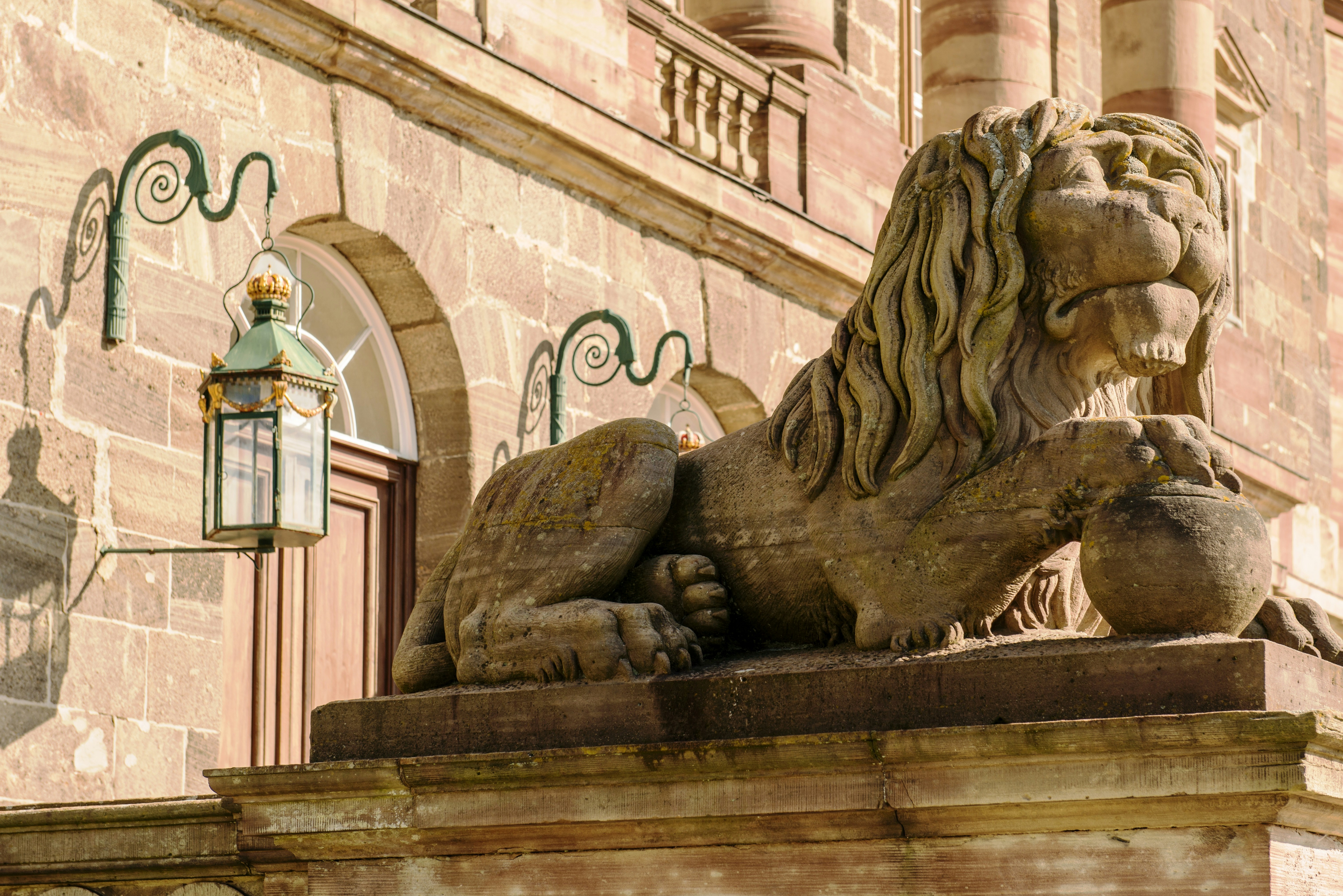 Majestic stone lion sculpture poised atop an ornate building entrance, bathed in warm sunlight.
