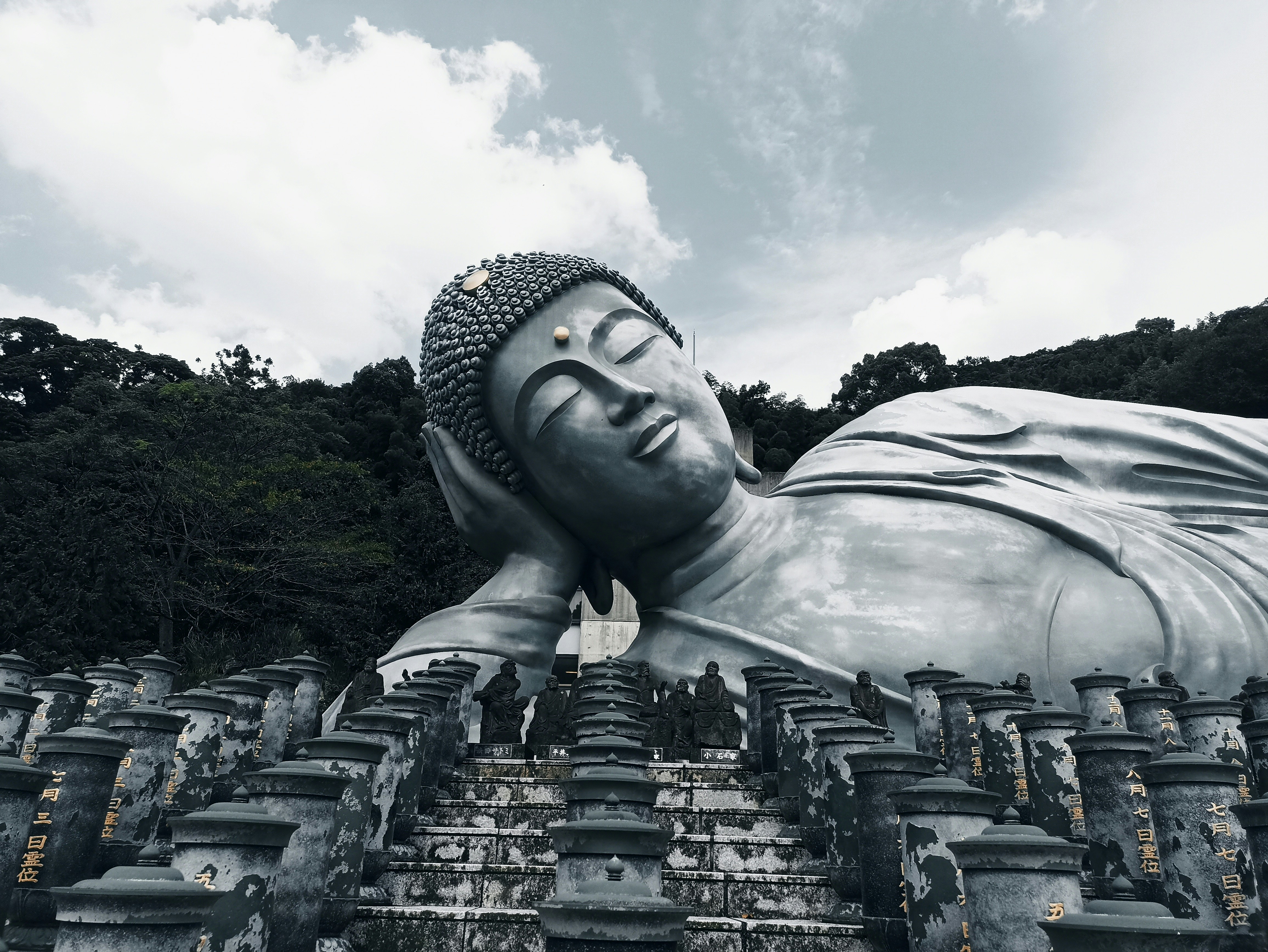 Reclining Buddha statue surrounded by stone offerings nestled in a lush landscape.