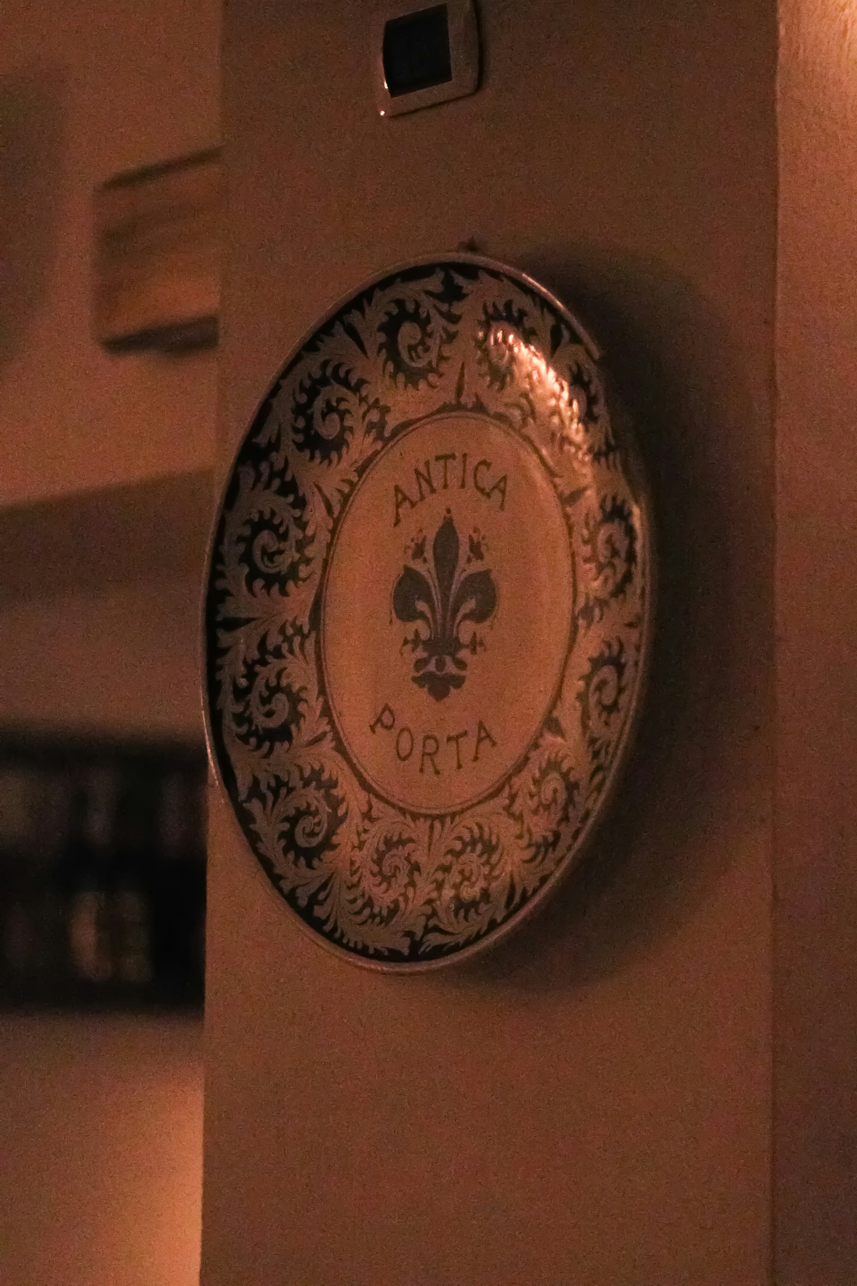 Decorative plate featuring the words 'ANTICA PORTA' and a floral design, mounted on a wall in a dimly lit setting.