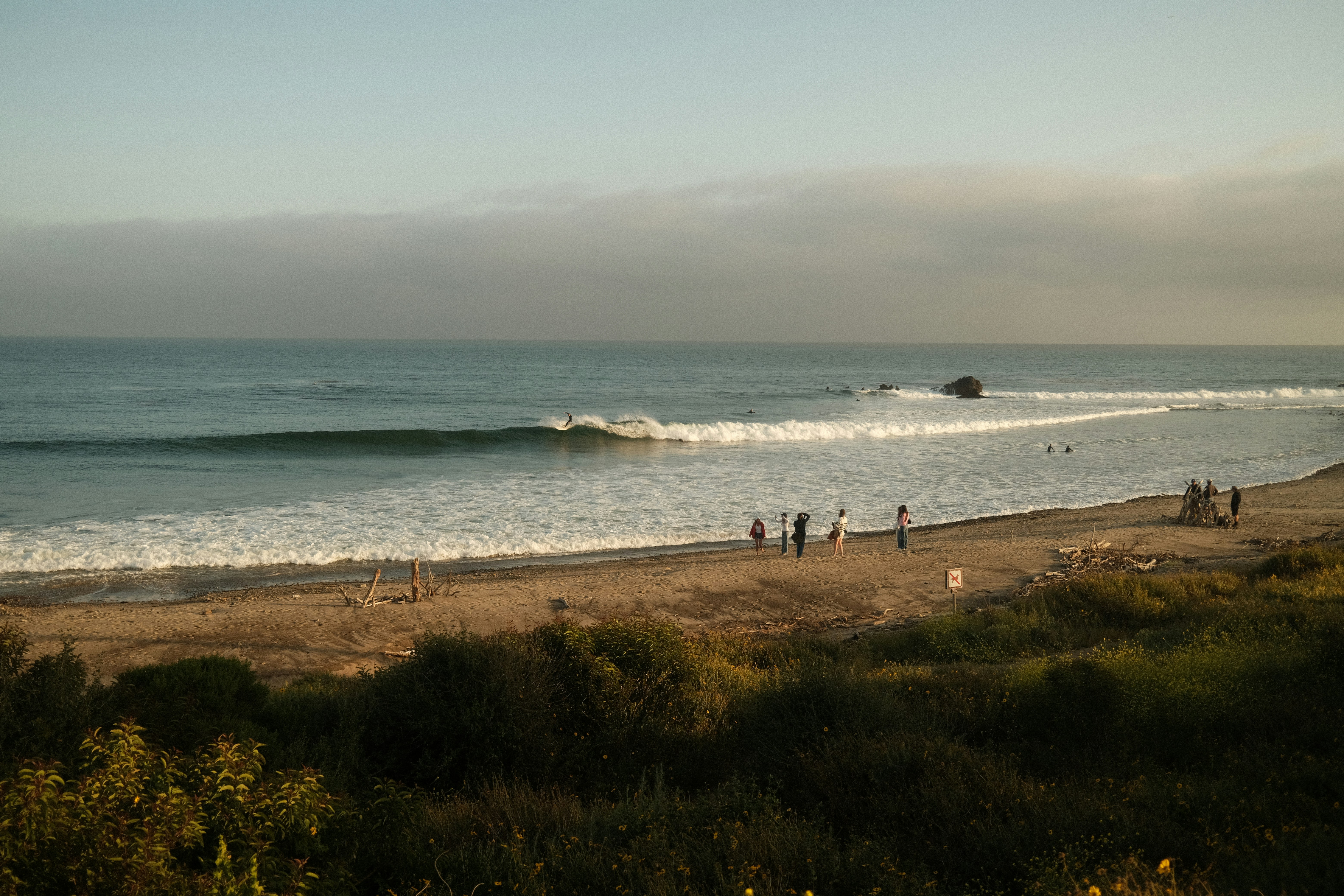 Sunlit Tide: A Small Crowd Along a Quiet Beach at Golden Hour