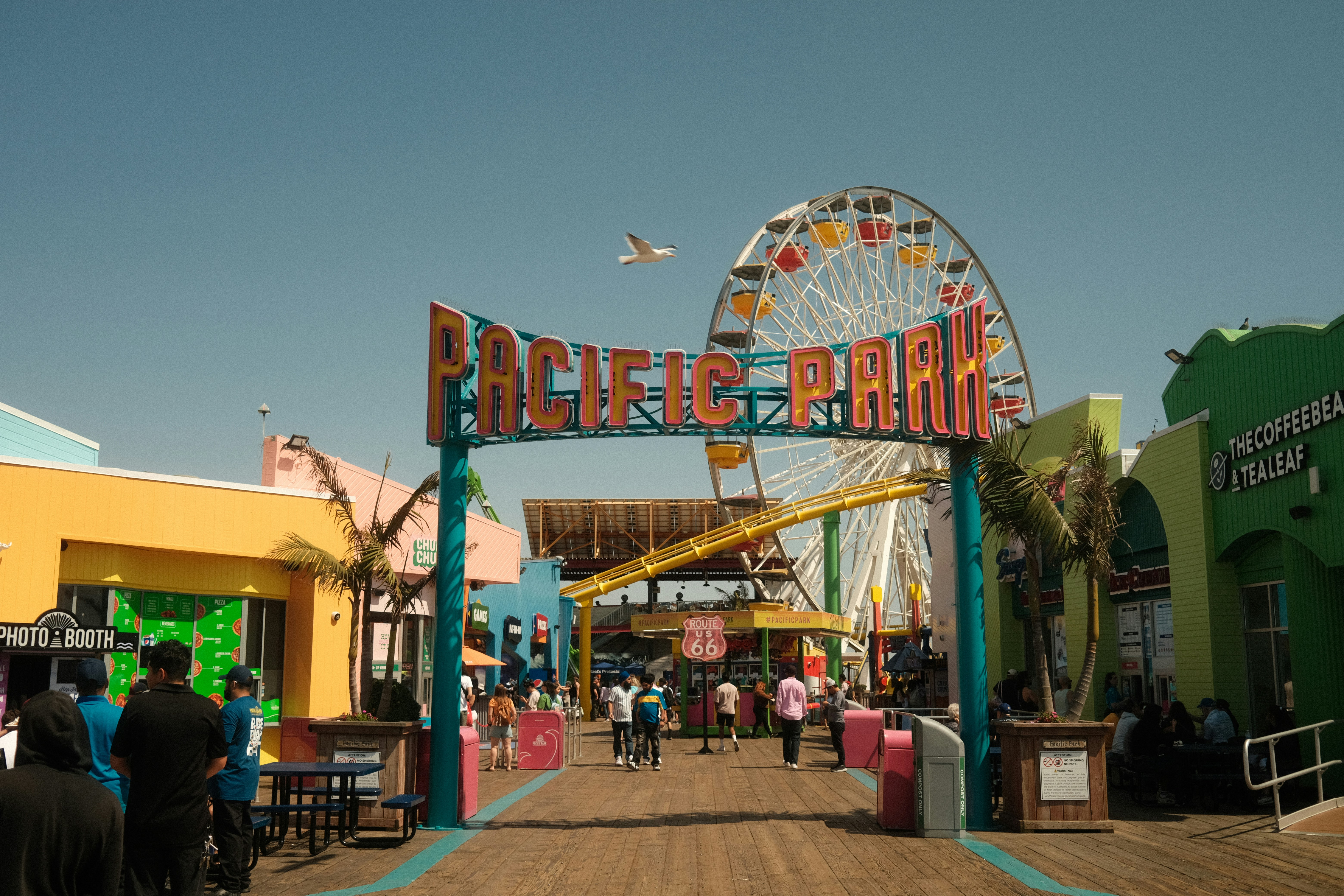 Colorful entrance to Pacific Park with a ferris wheel in the background, bustling with visitors enjoying a sunny day.