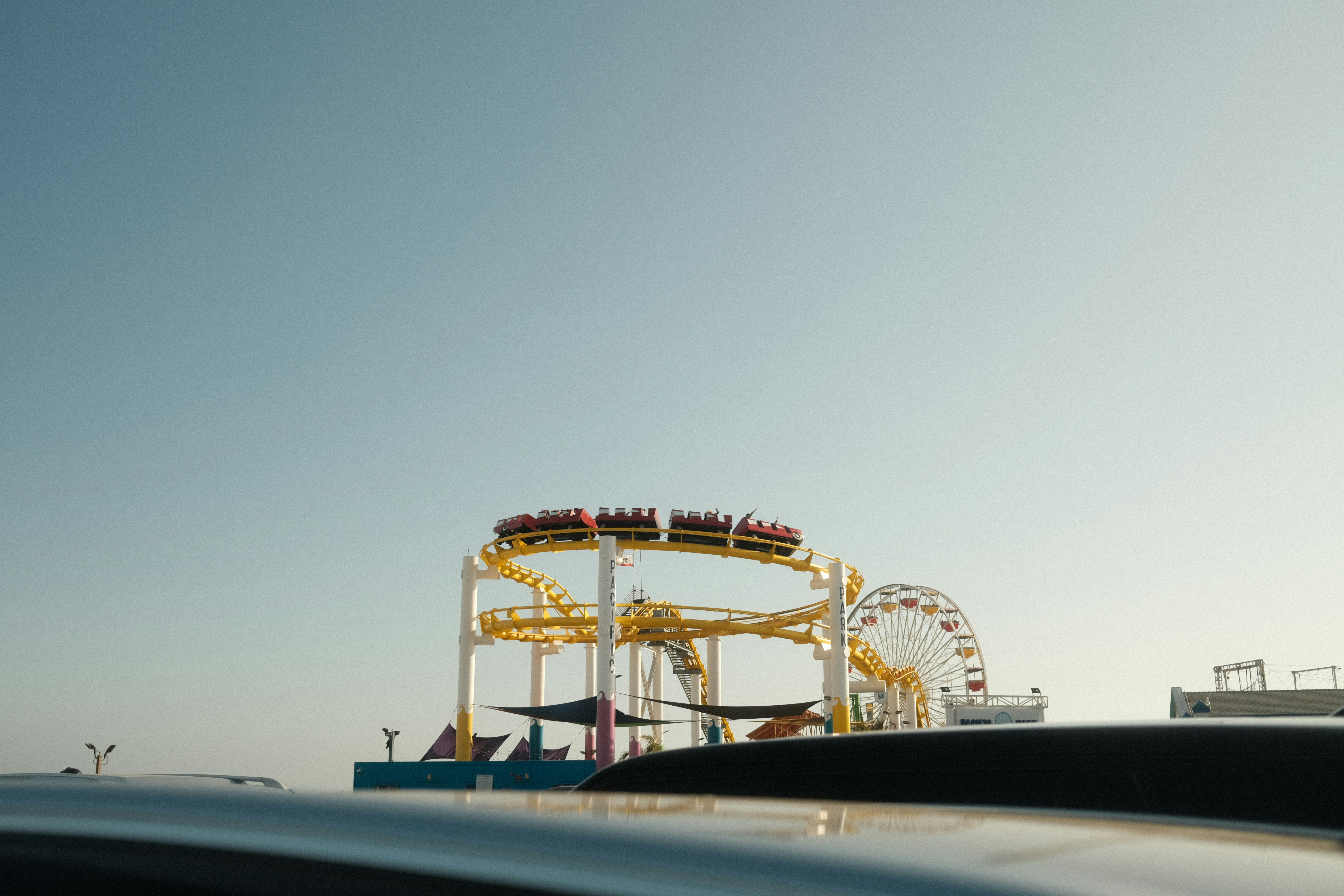 Dashboard Vista: Yellow Roller-Coaster Framework Framing a Distant Ferris Wheel