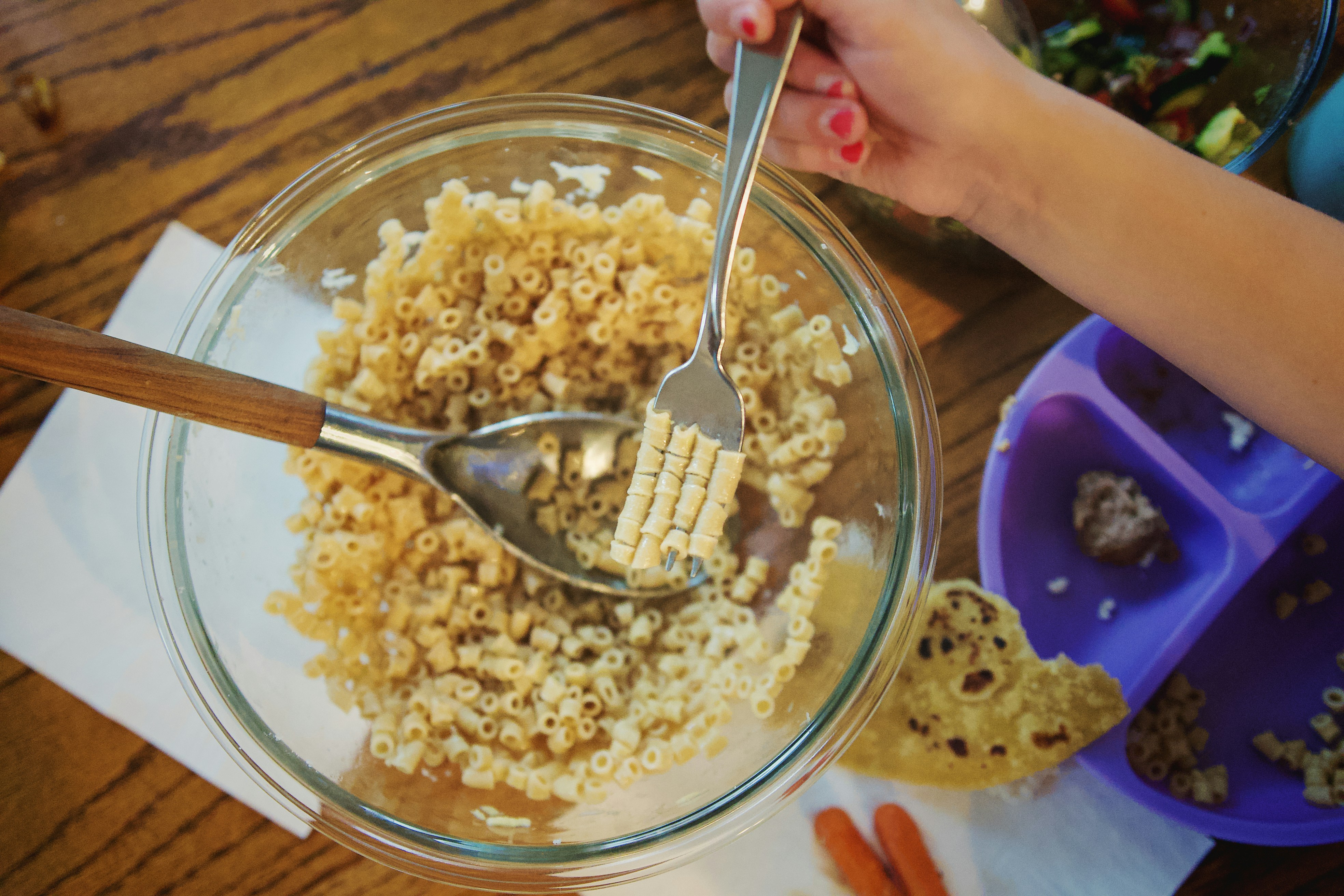 Twirl of elbow macaroni: a quiet kitchen moment above a glass bowl