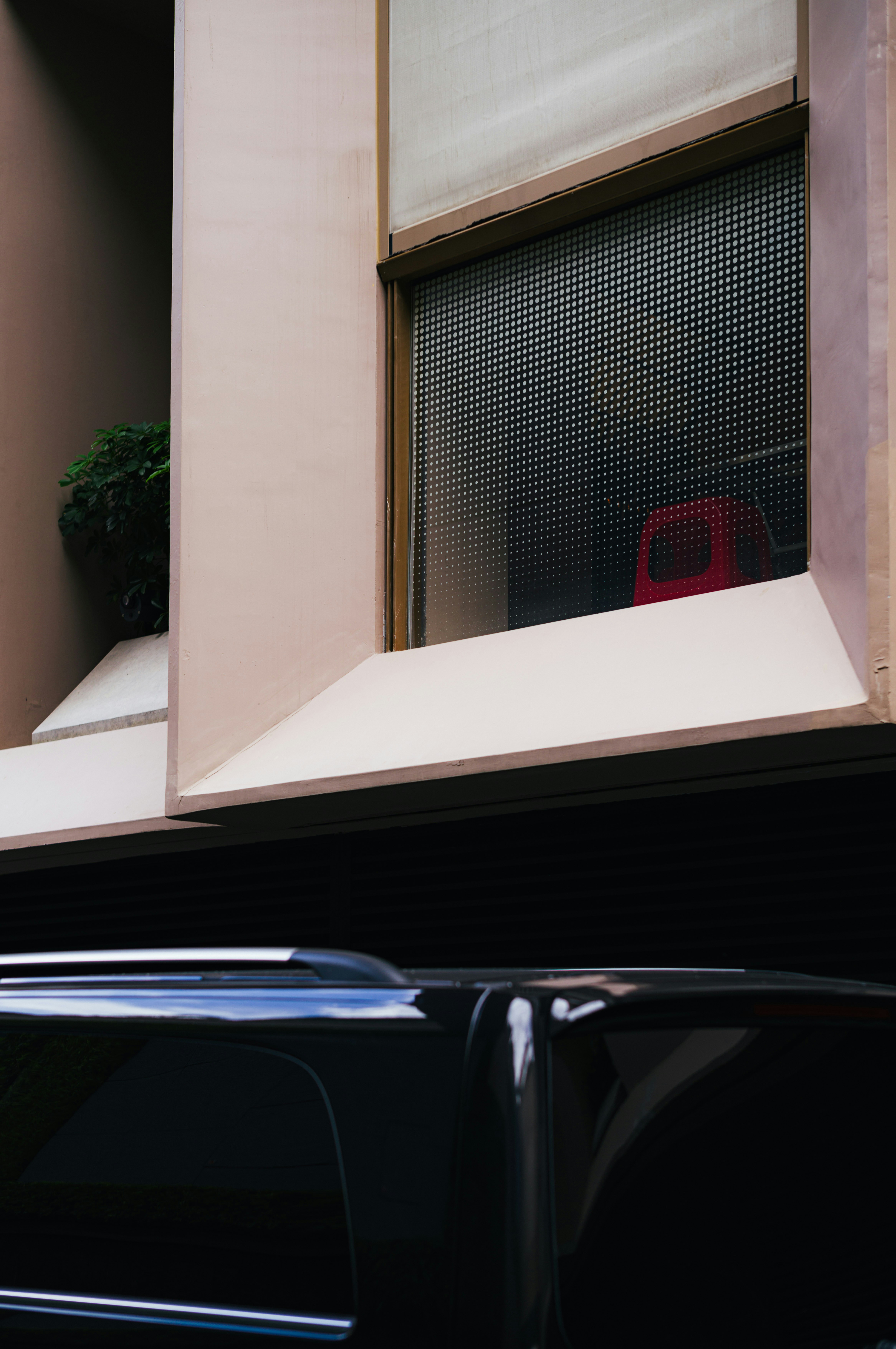 Dotted-Glass Window Framed by Beige Geometry Over a Gleaming Car Roof