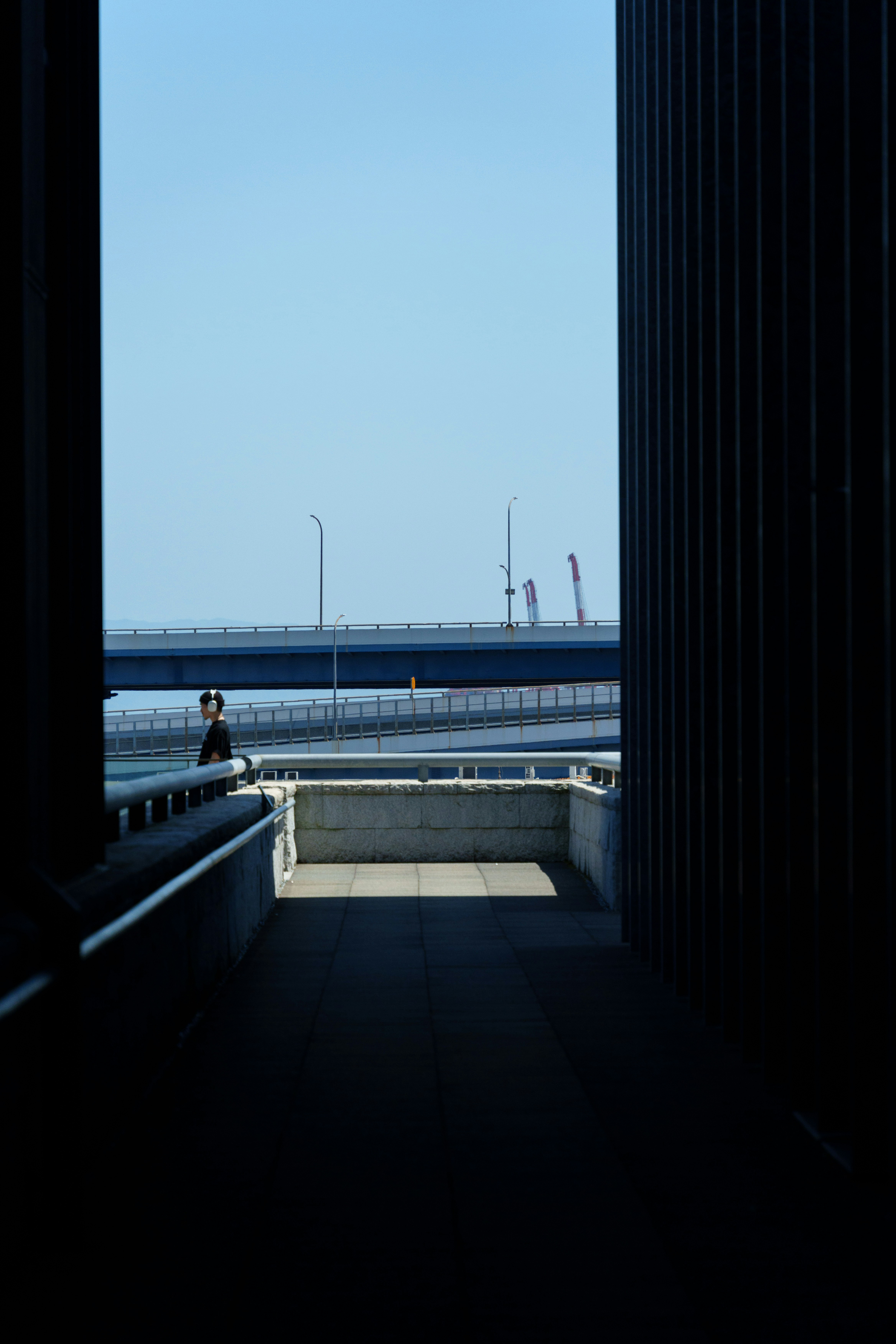 Through the Narrow Gloom: A lone pedestrian anchored by a stark urban corridor toward a sunlit skyline