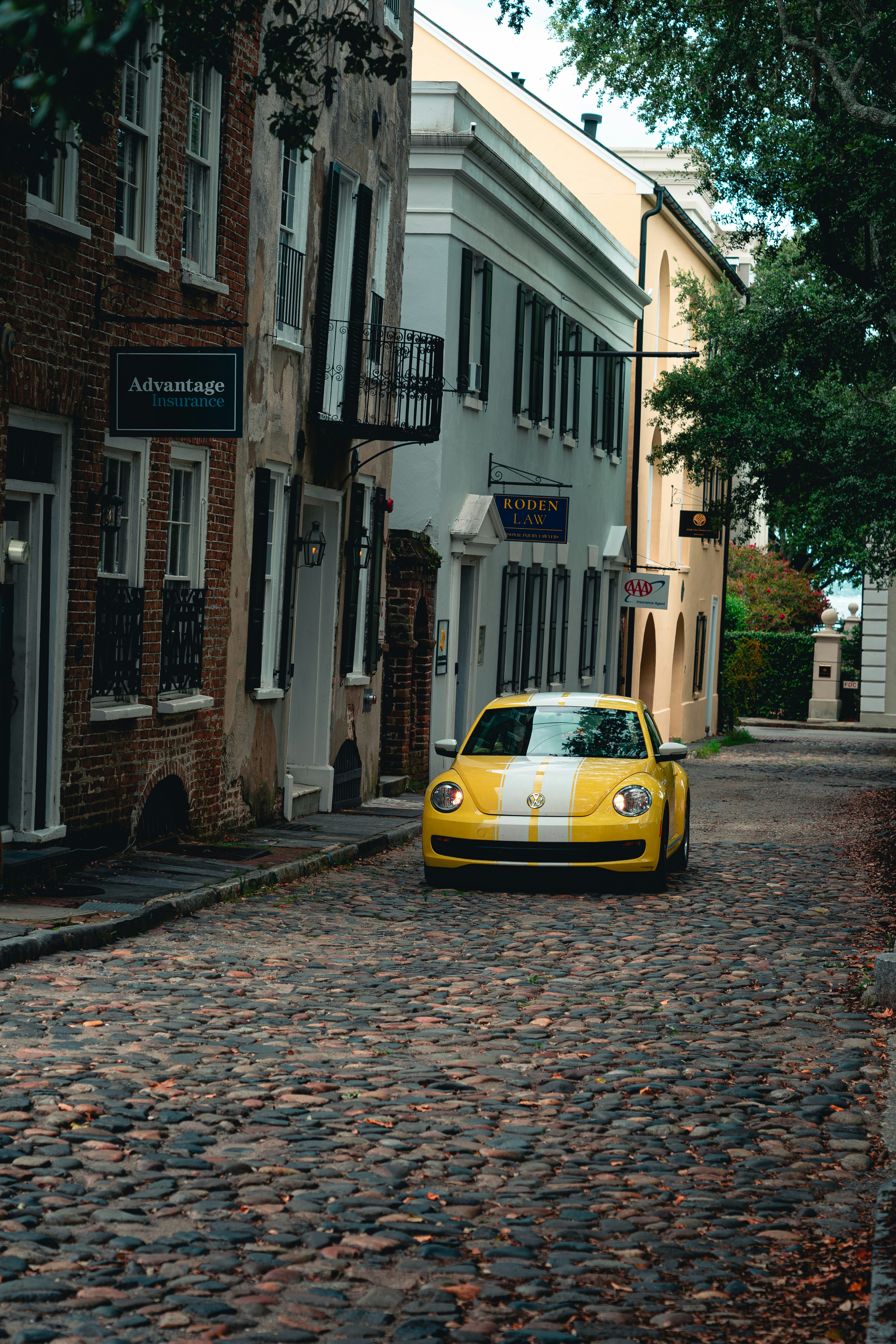 Yellow car parked on a cobblestone street lined with historic buildings and trees.
