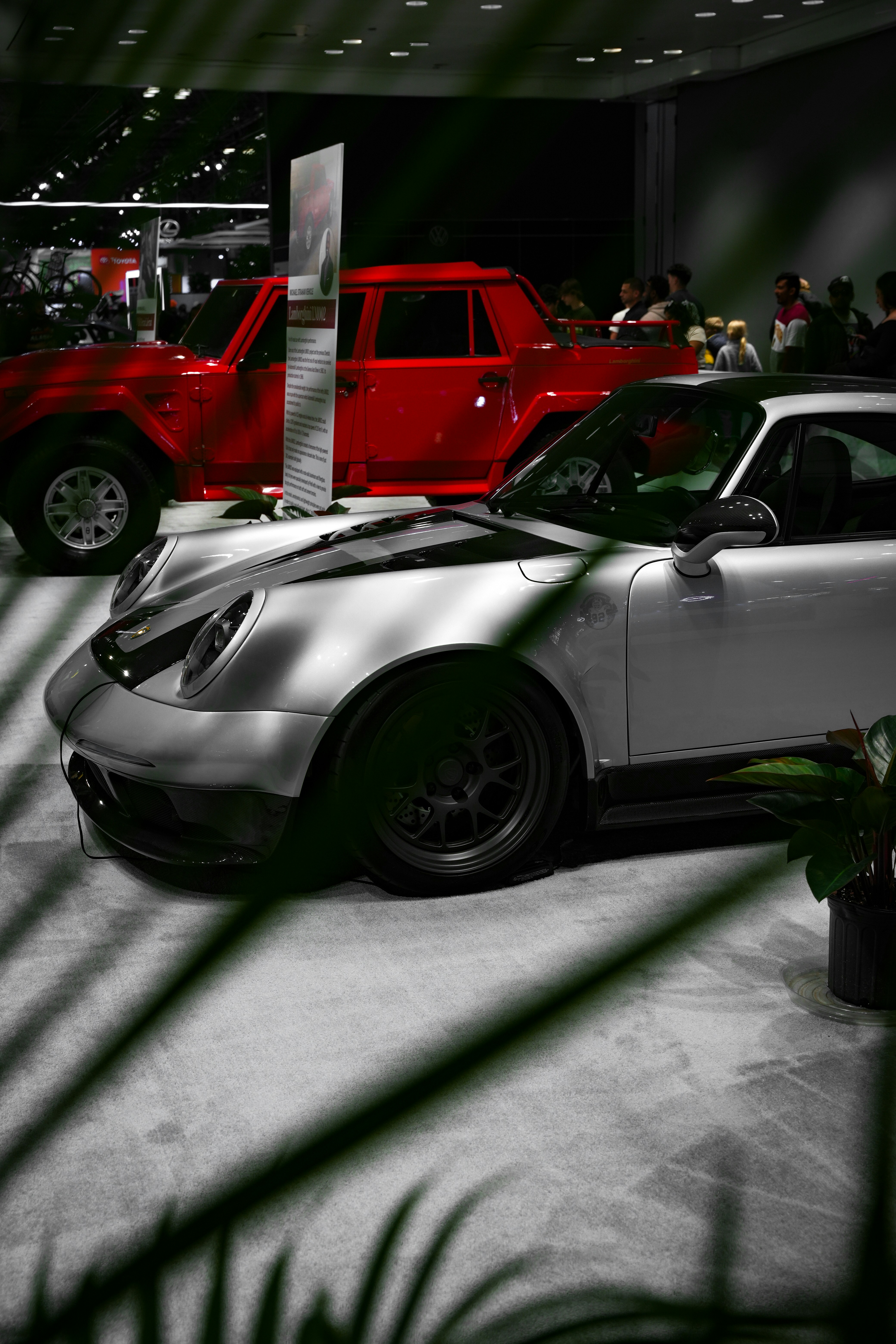 Silver Porsche Takes Center Stage Among Crimson SUVs at a Dim Auto Show