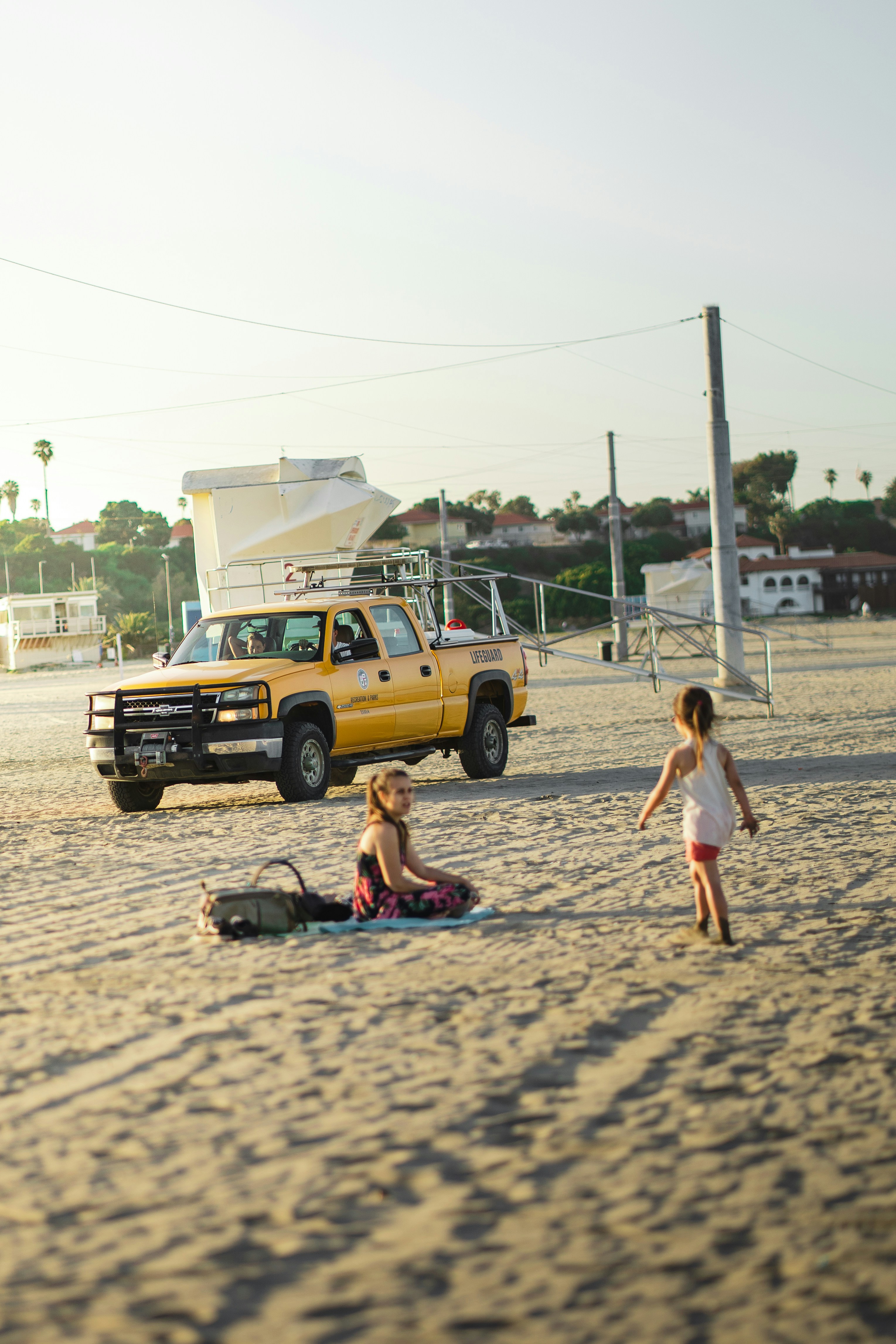 Golden Hour on the Sand: A Yellow Lifeguard Truck and Two Girls at Play