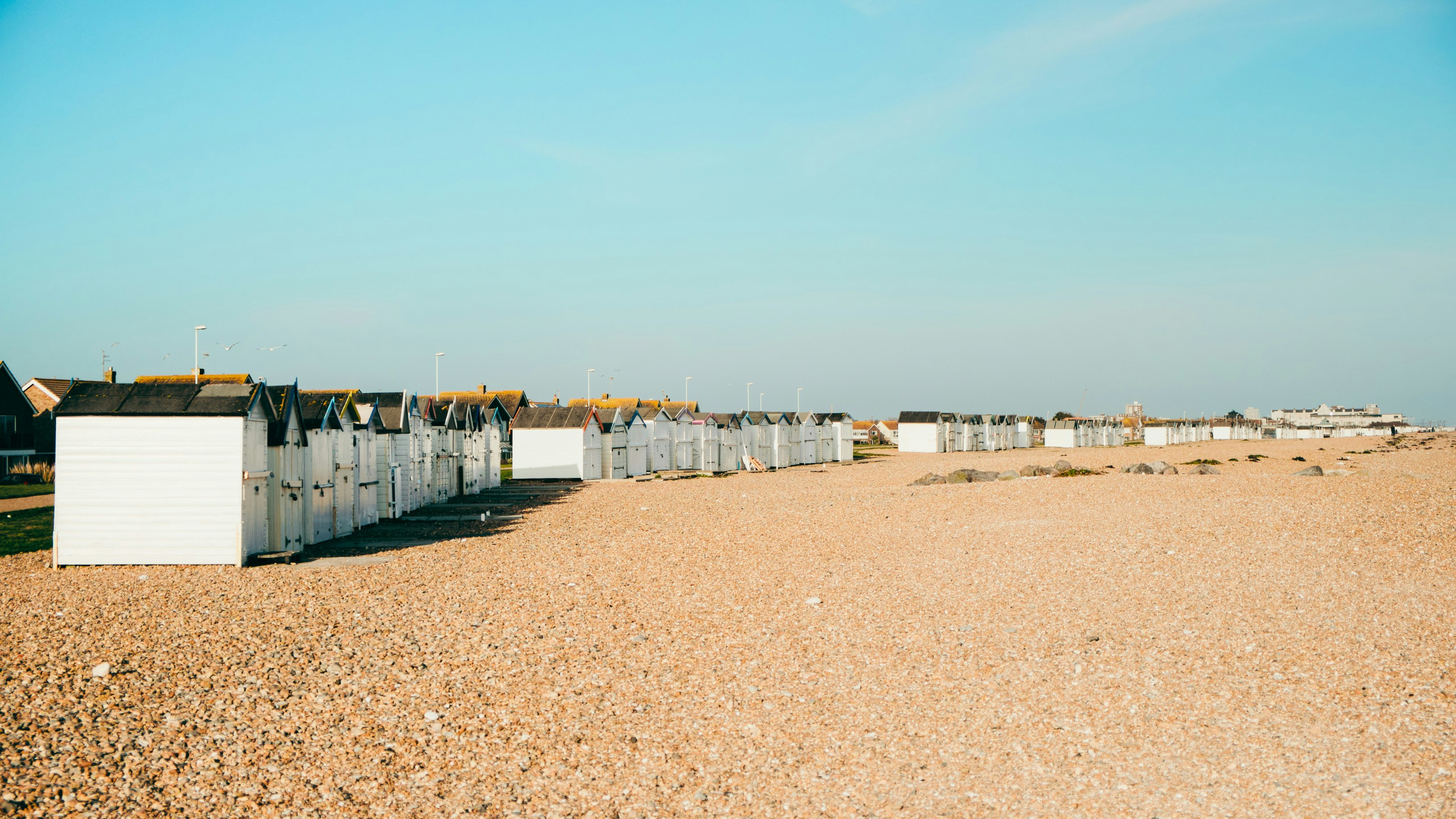 A row of beach huts sitting on top of a sandy beach photo – Free Blue ...