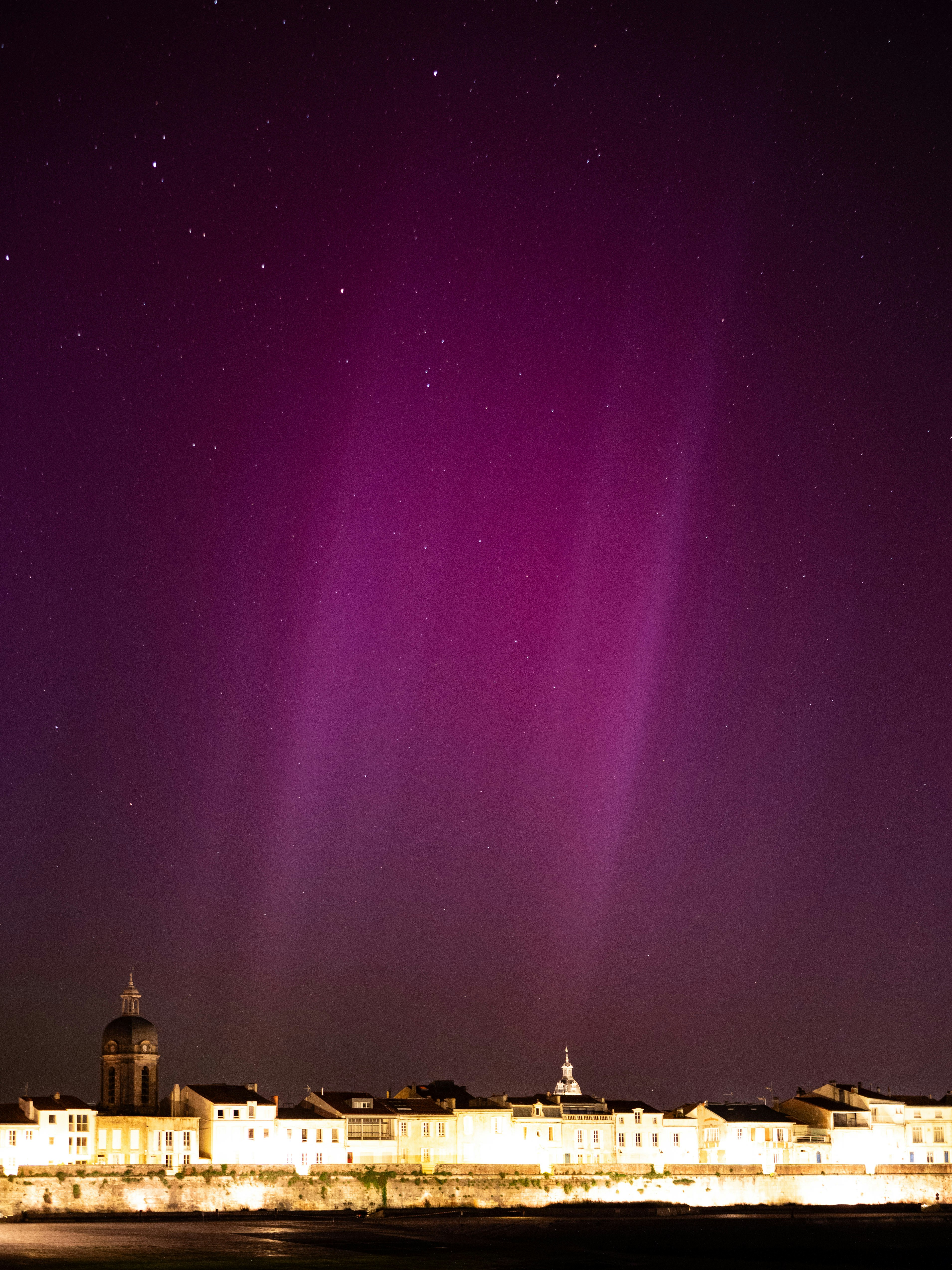 Aurora over the riverfront: a magenta night sky above a quiet town