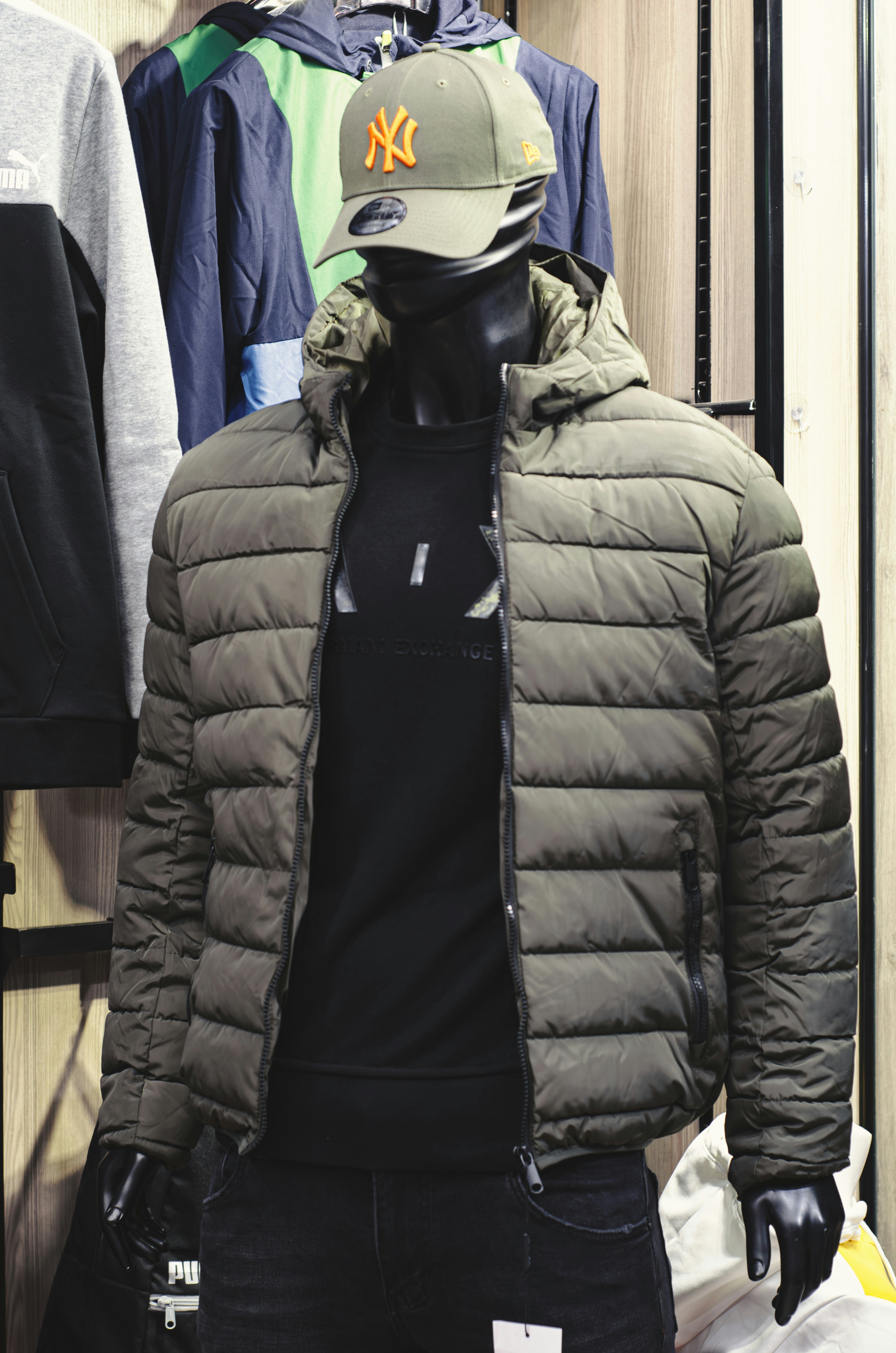 Layered Quiet: Khaki Puffer Jacket on a Shadowed Mannequin in a Boutique Window