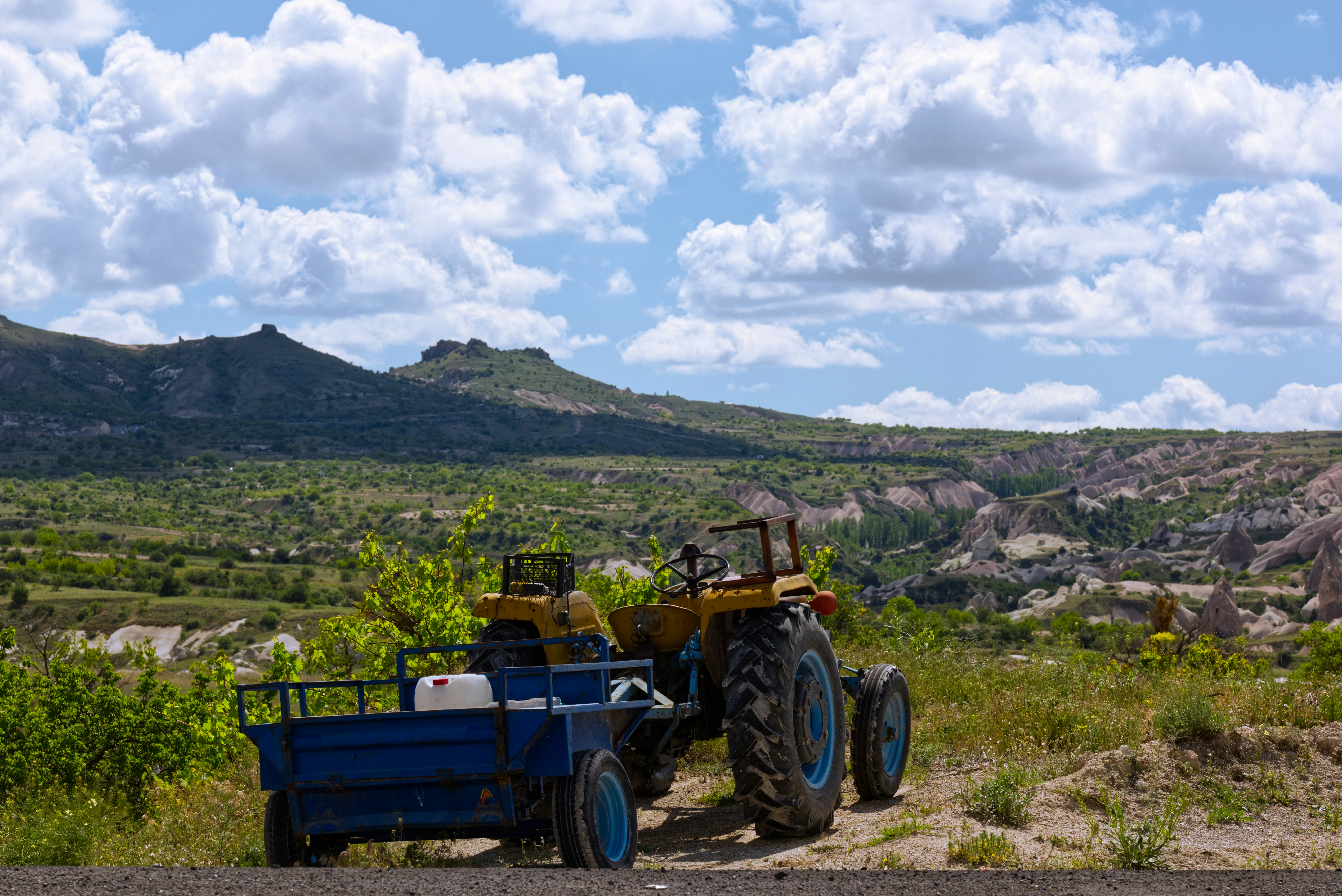 Sunlit Southwestern Meadow: Yellow Tractor with Blue Trailer in Rolling Hills