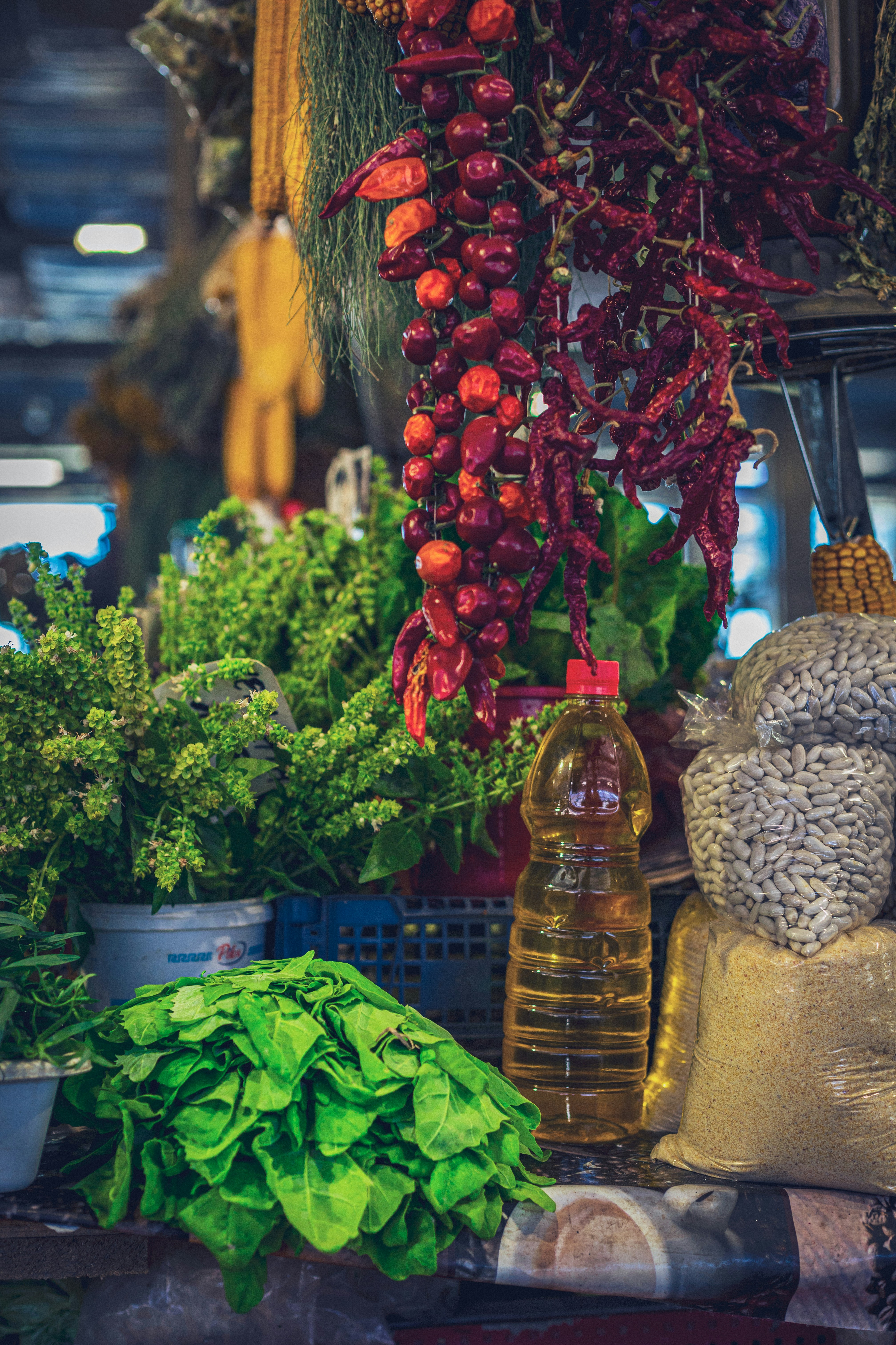 Harvest Mosaic: Greens, Red Chilies, and an Amber Oil Bottle in a Busy Market Stall