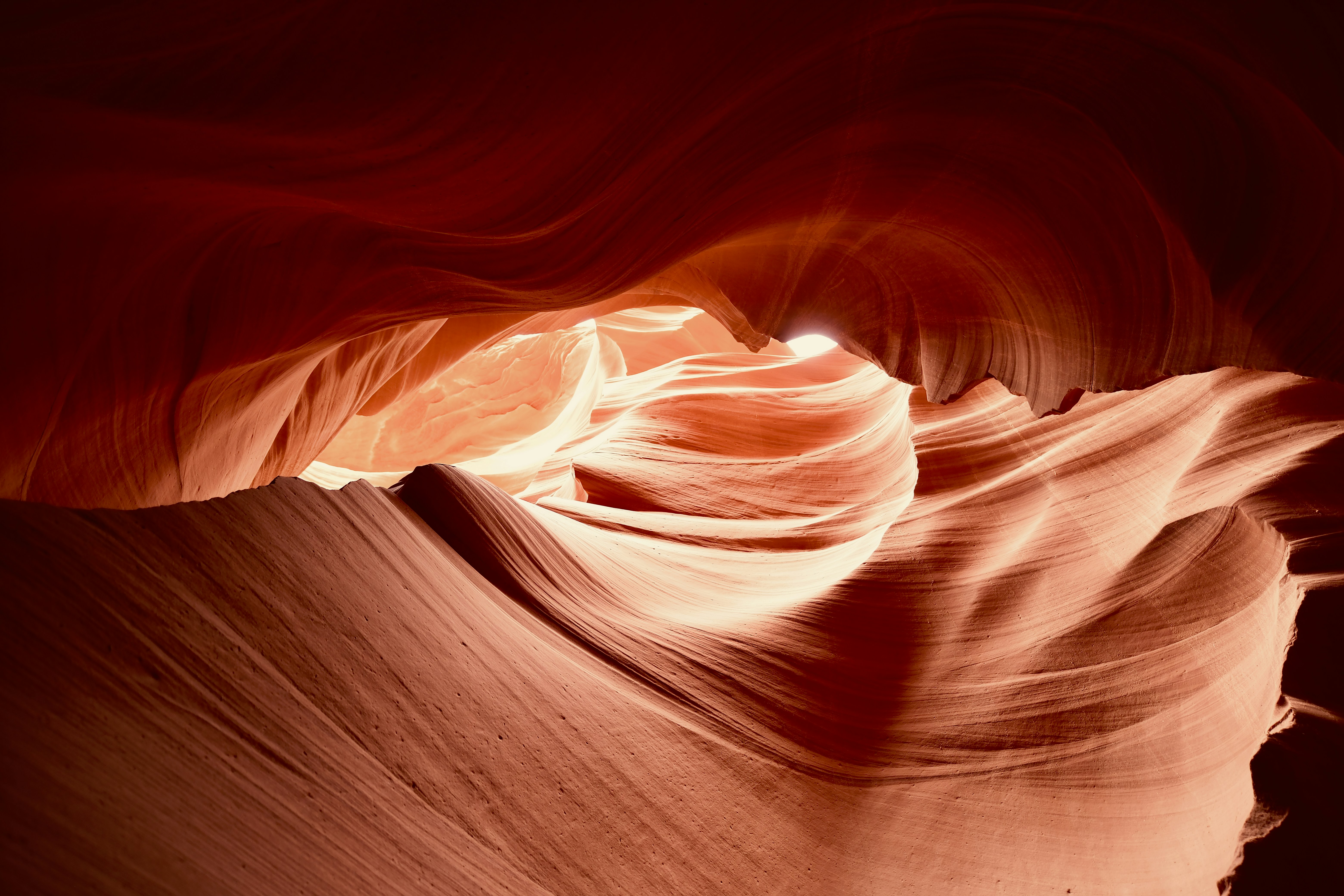 Sunlight illuminates the swirling sandstone curves of Antelope Canyon in warm shades of red and orange.