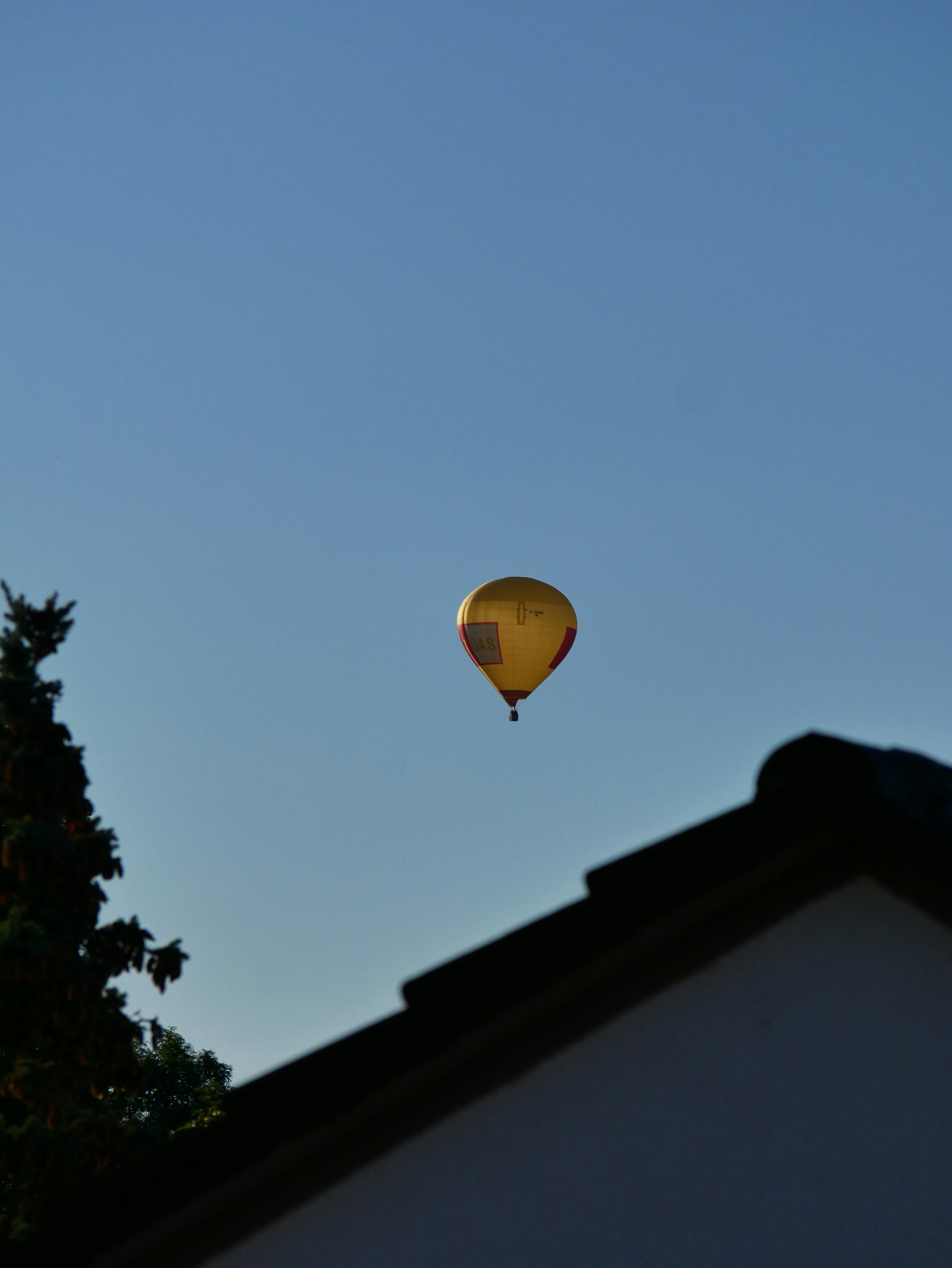 Sunlit Yellow Balloon Traverses the Skyline Above a Gabled Rooftop