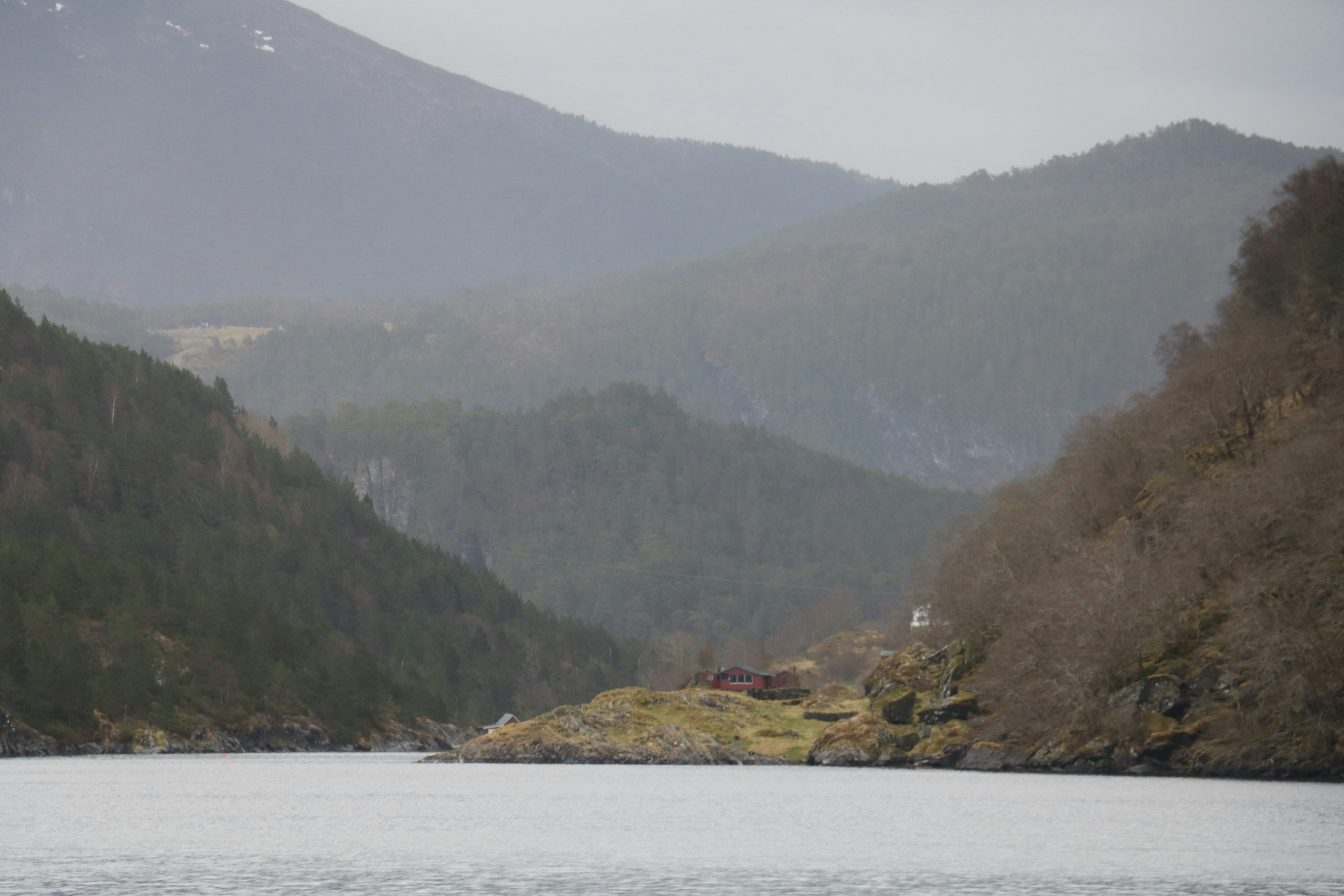 Quiet fjord of distant hills with rocky outcrop and a small red structure