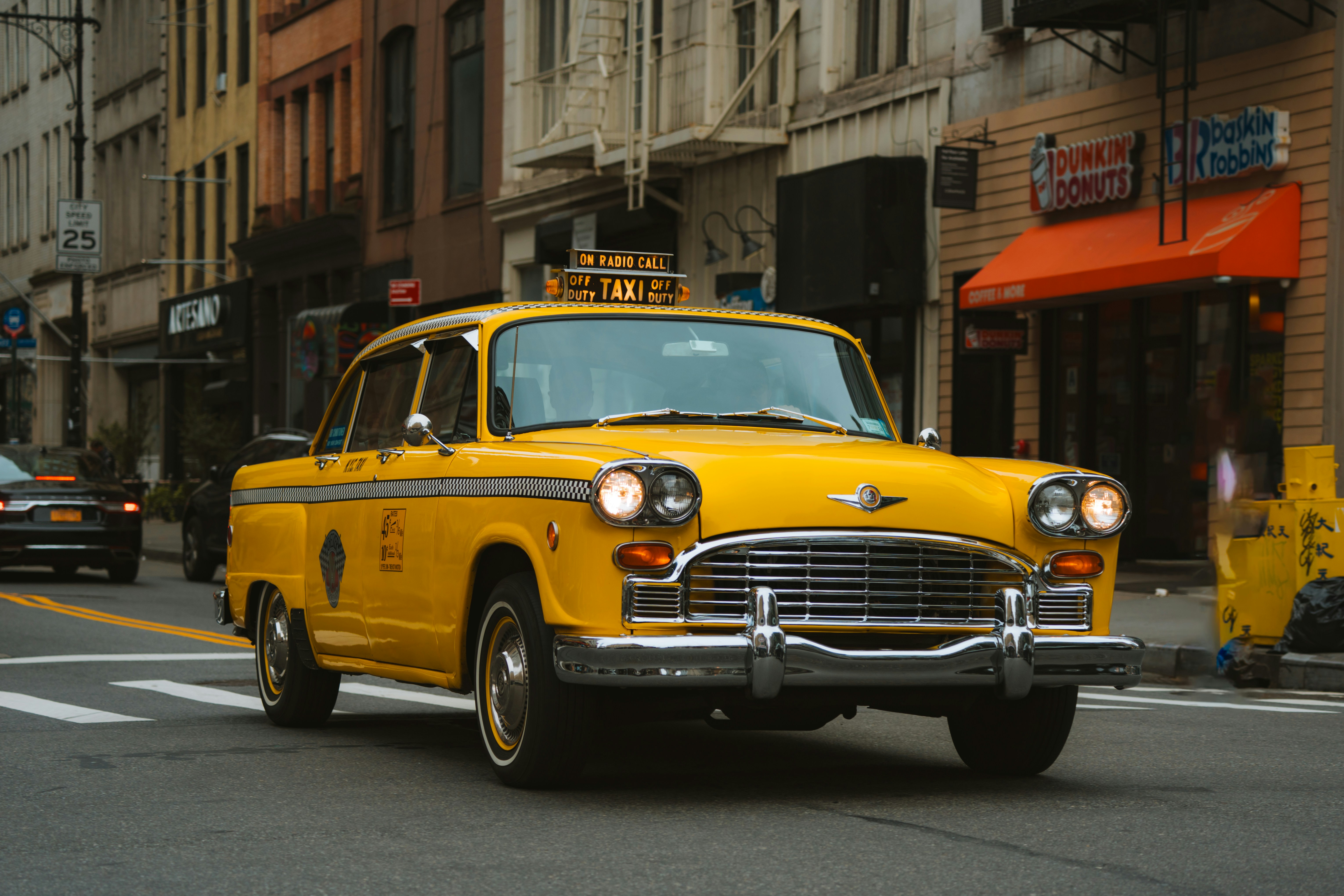 A yellow taxi cab driving down a street next to tall buildings photo ...