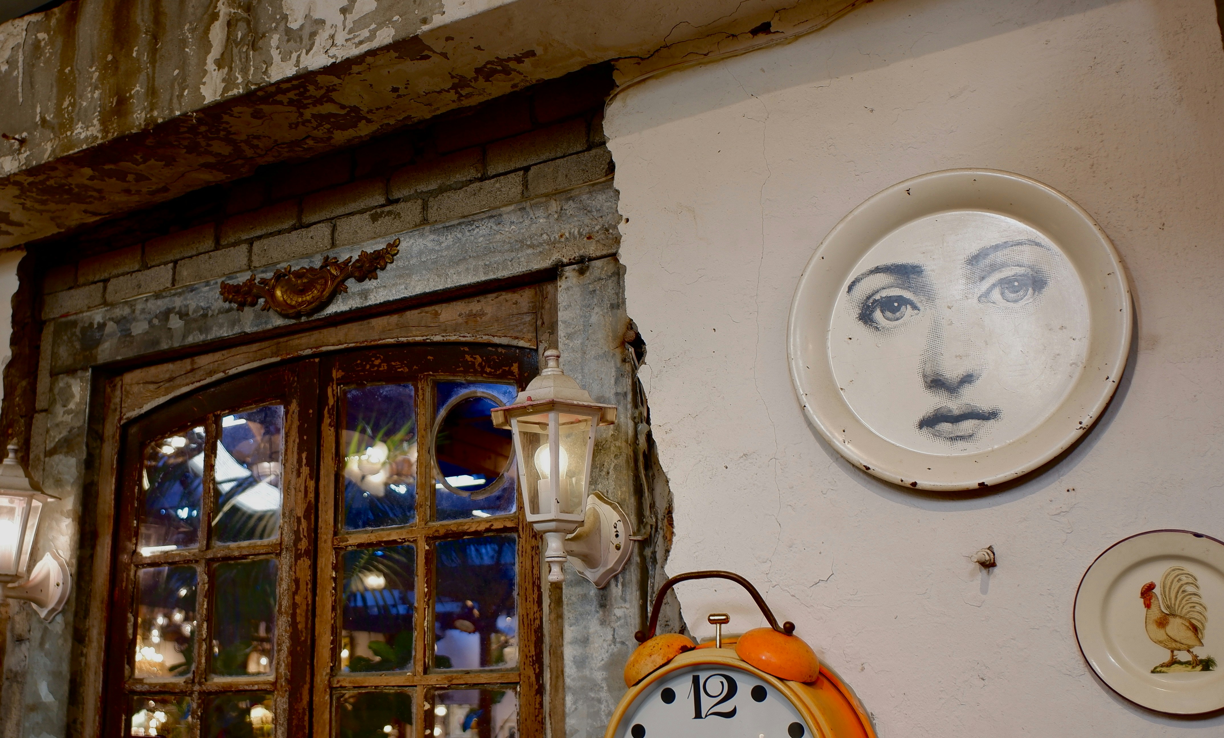 Decorative wall scene featuring a circular plate with a face, a vintage clock, and a windowed door with stained glass panels in a rustic setting.