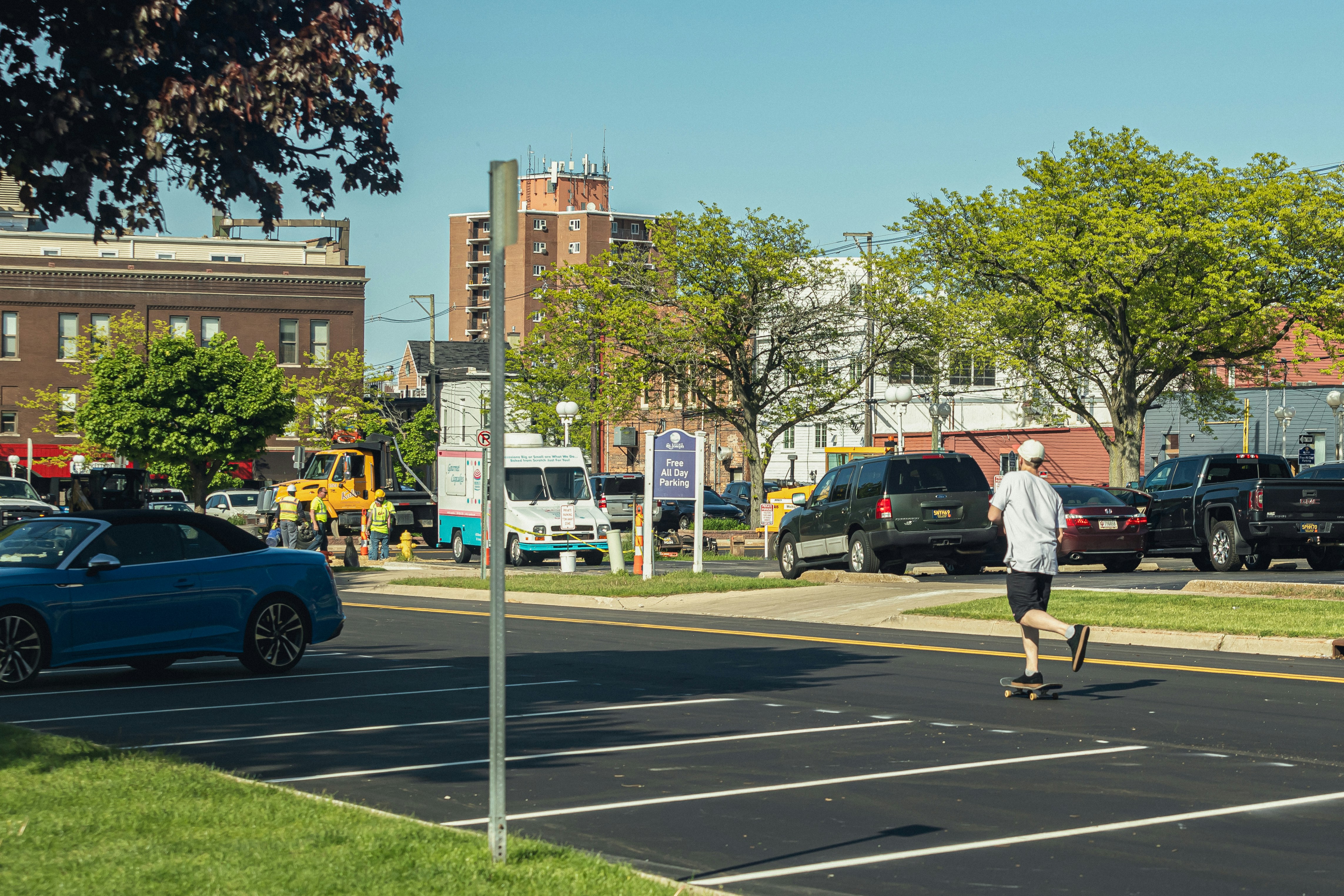 Skateboarder gliding through a city parking lot with construction and parked cars in the background.