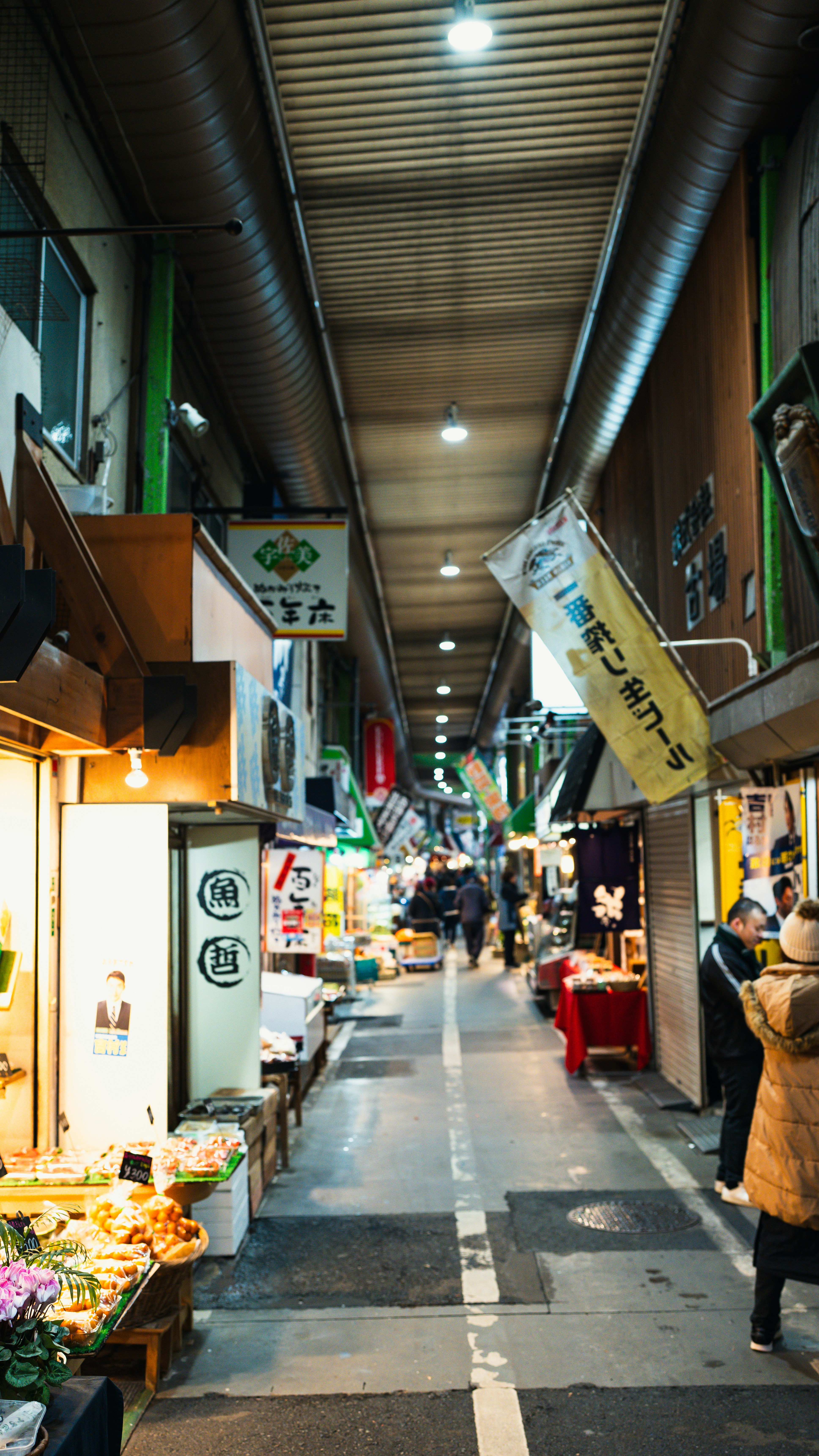 Narrow market alley with colorful signs and bustling shops under warm lighting.
