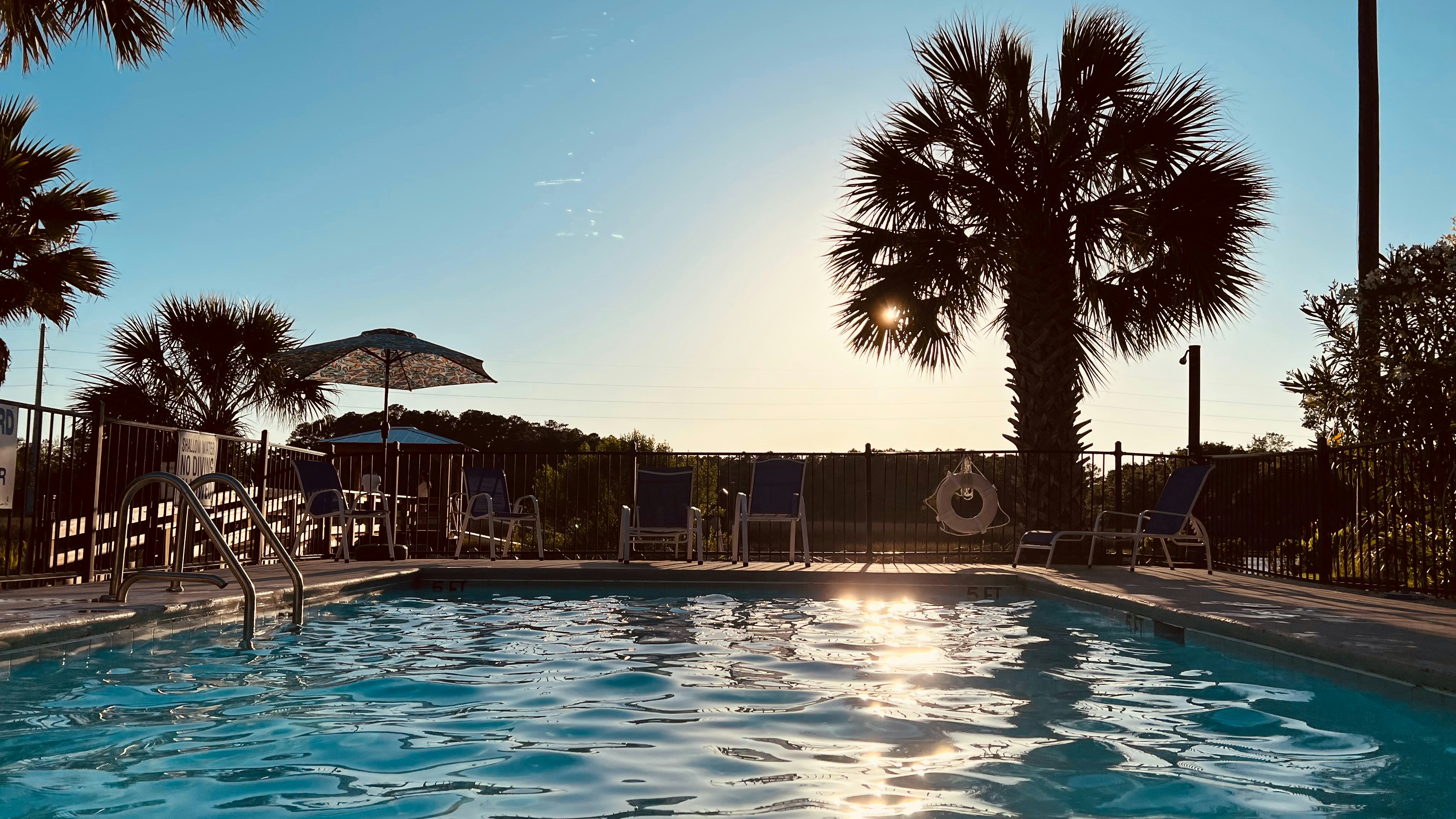 Serene motel pool reflecting the warm hues of a setting sun with silhouetted palm trees.