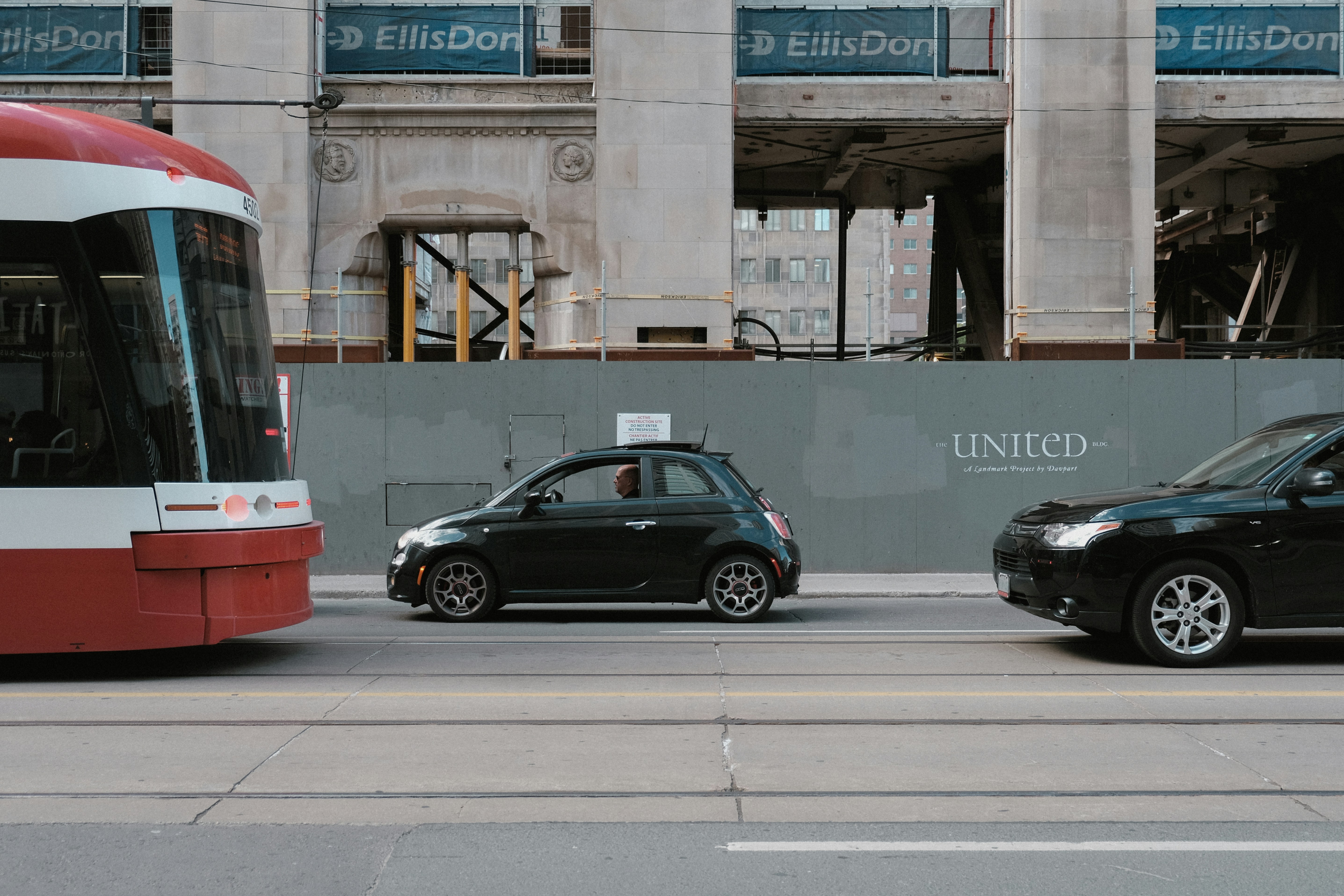 Urban Transit in Focus: A Black Car Between a Red-Front Tram and City Wall