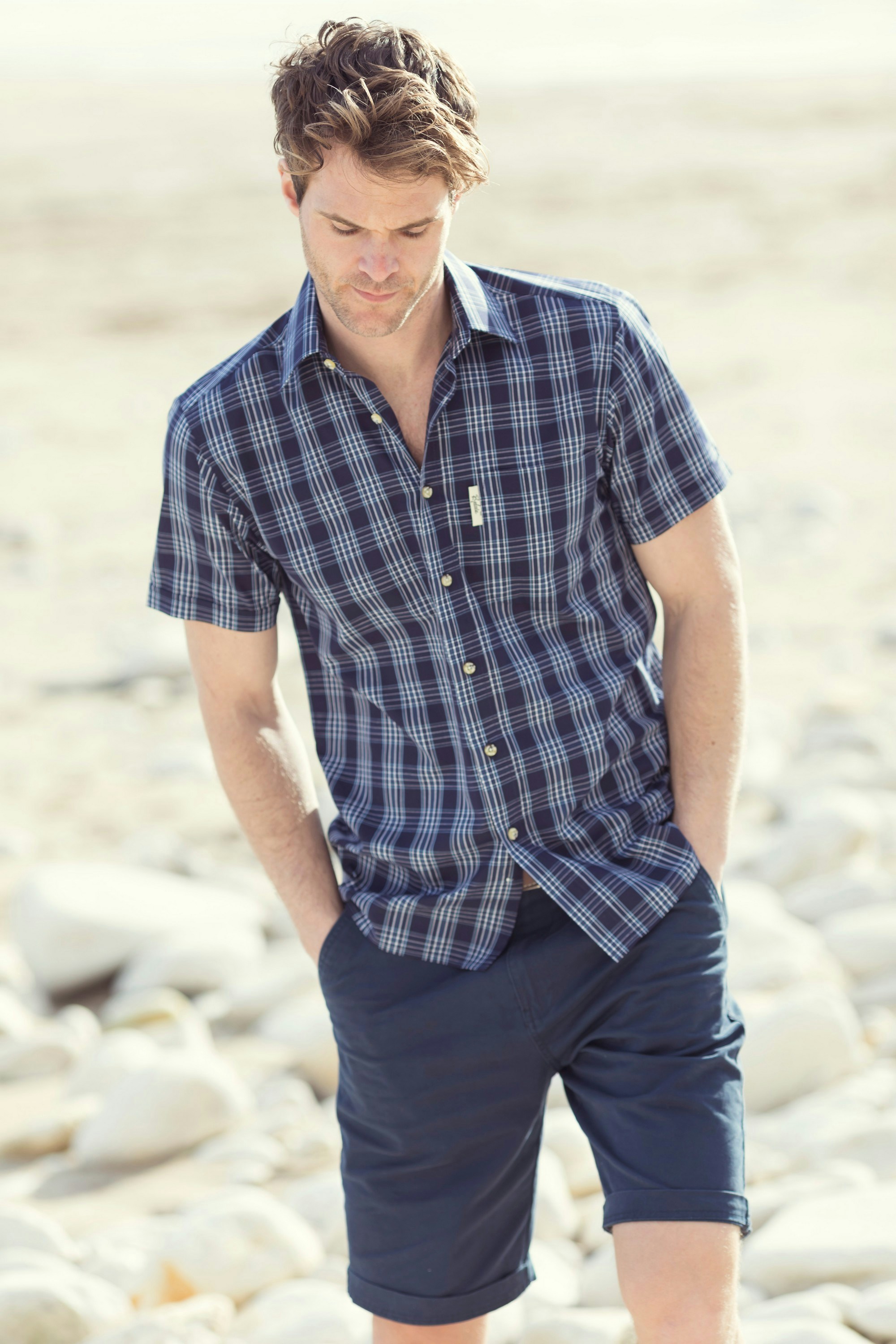 Coastal Quiet: A man in blue plaid on a sunlit pebble beach