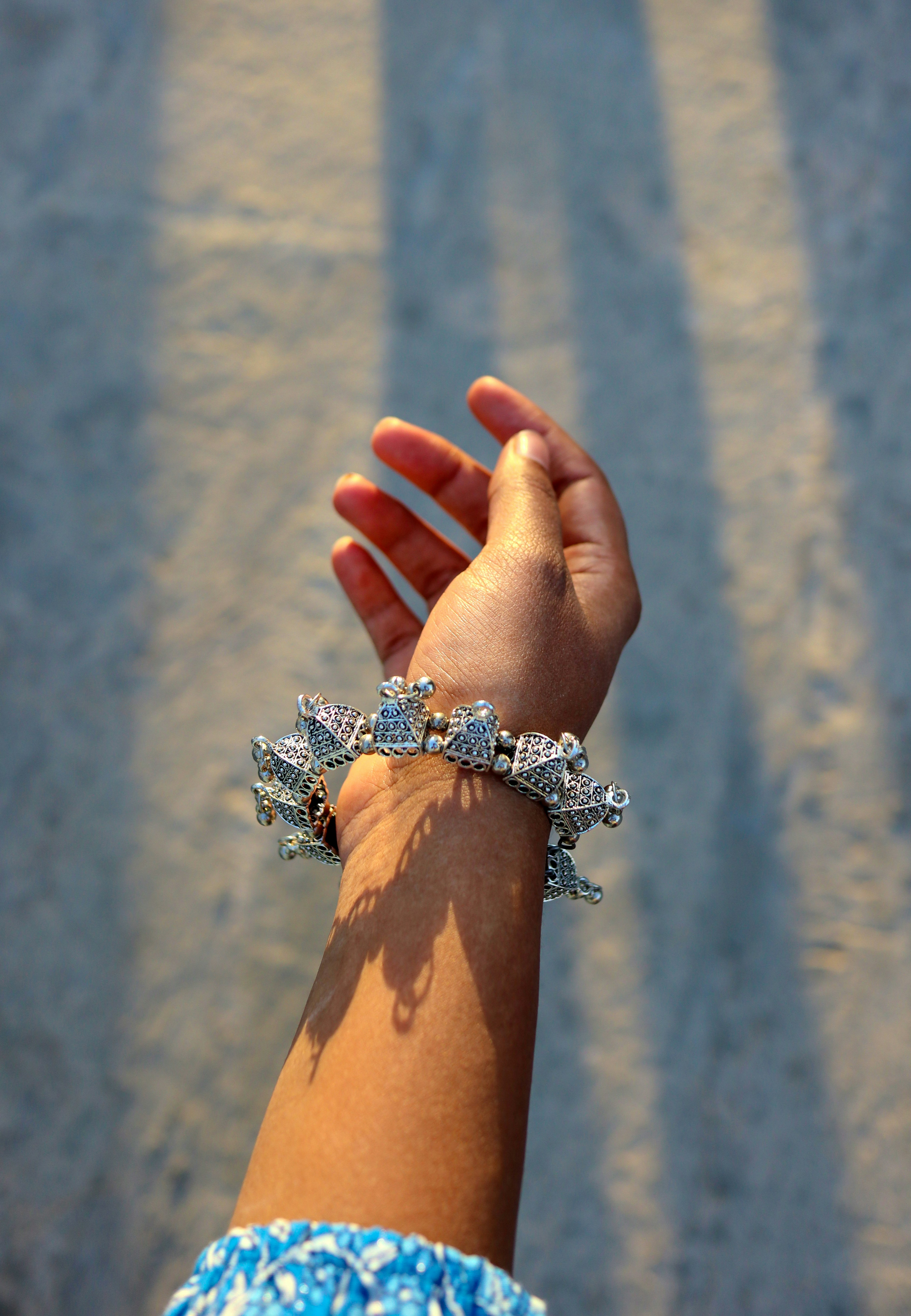 Delicate silver bracelet adorned with intricate designs resting on a hand, casting a soft shadow on a textured surface.