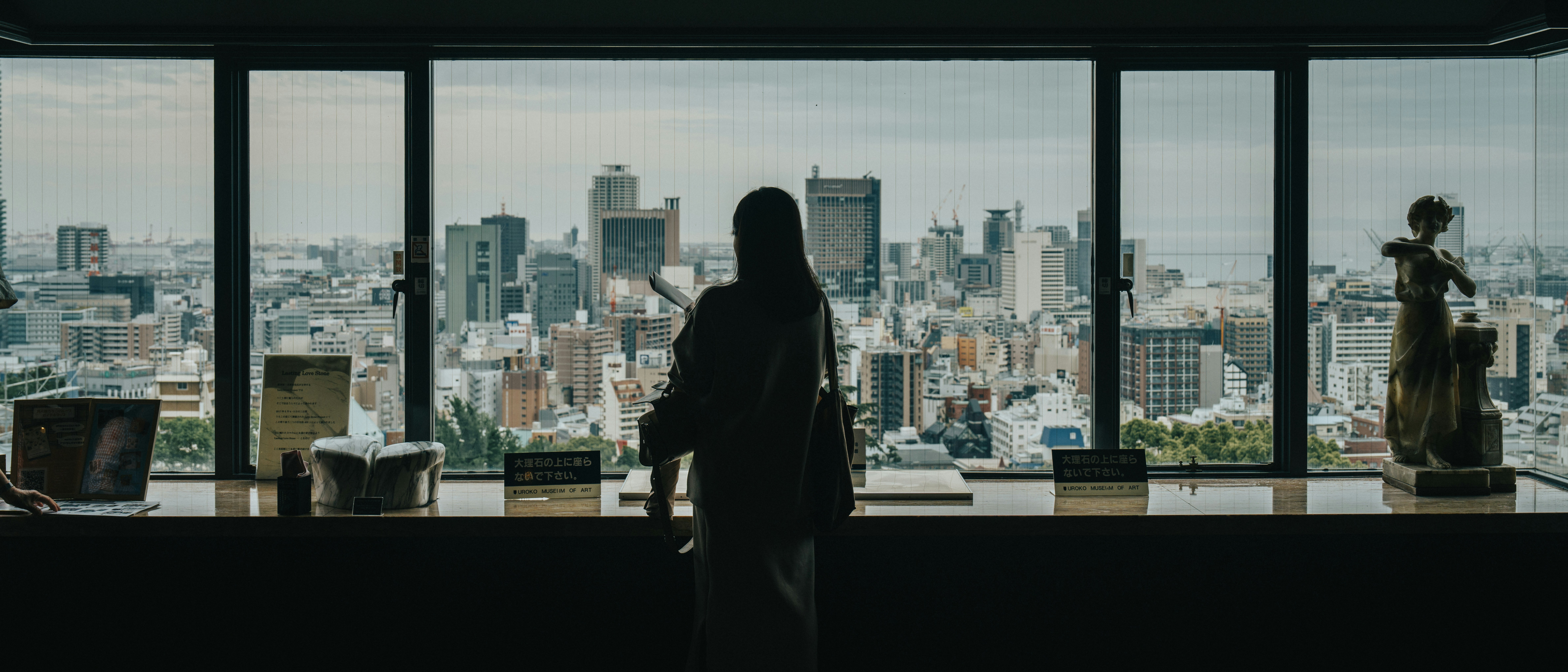 A woman standing in front of a window looking out at a city photo ...