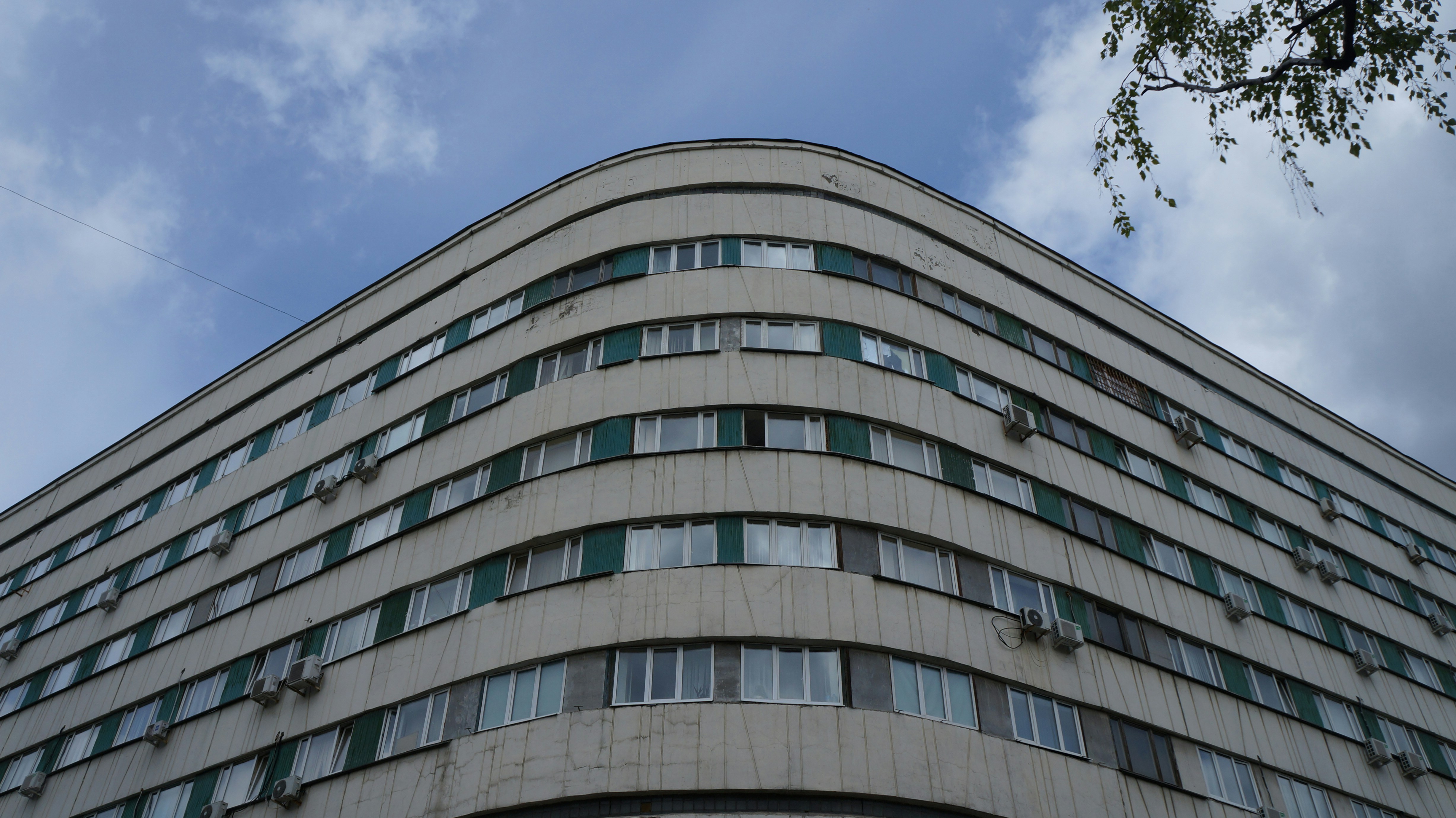 Architectural detail of a building featuring a smooth, curved facade with rows of windows and air conditioning units. The sky adds a contrasting backdrop.
