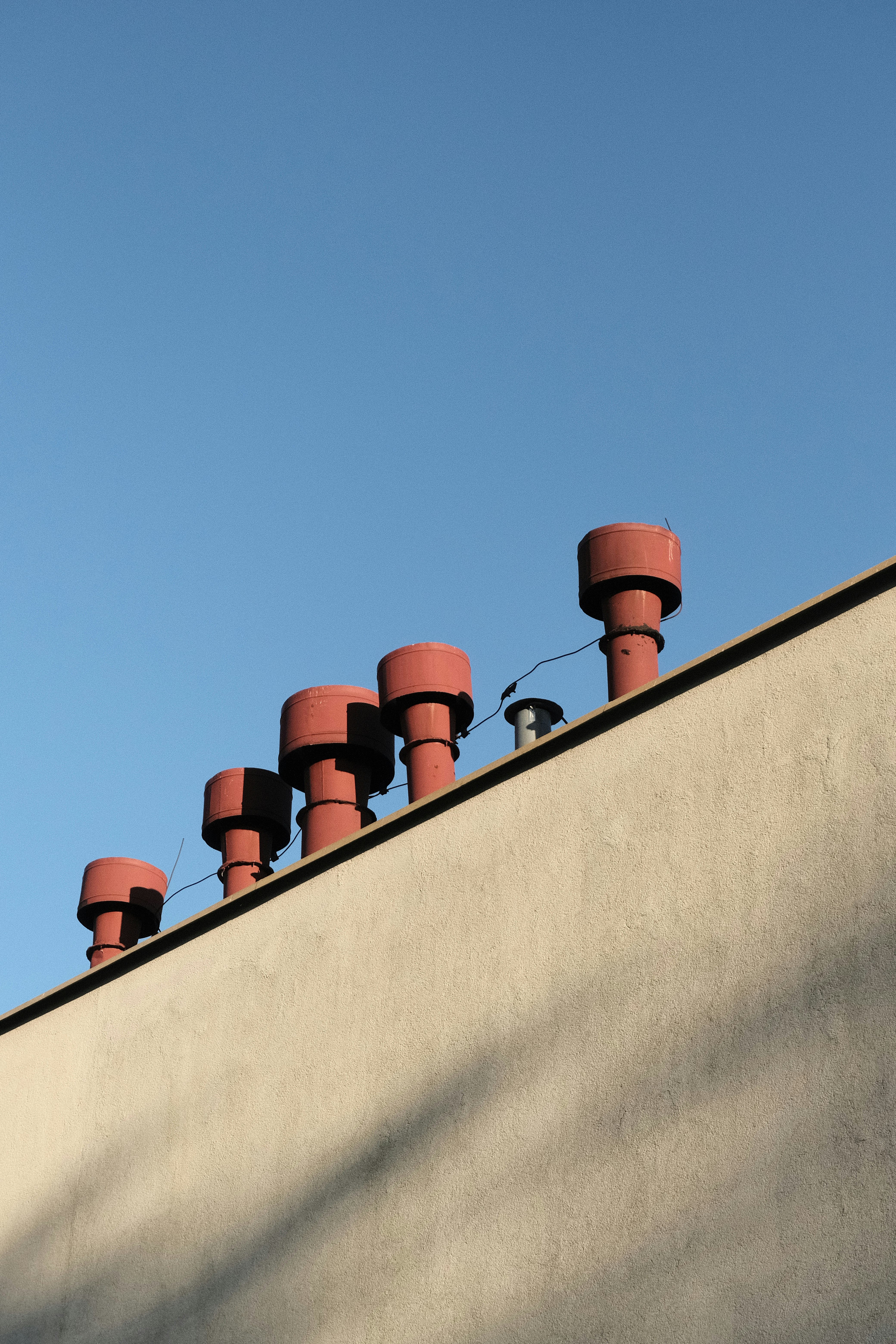 Row of Red Chimney Caps Along a Sunlit Roof Under Clear Sky