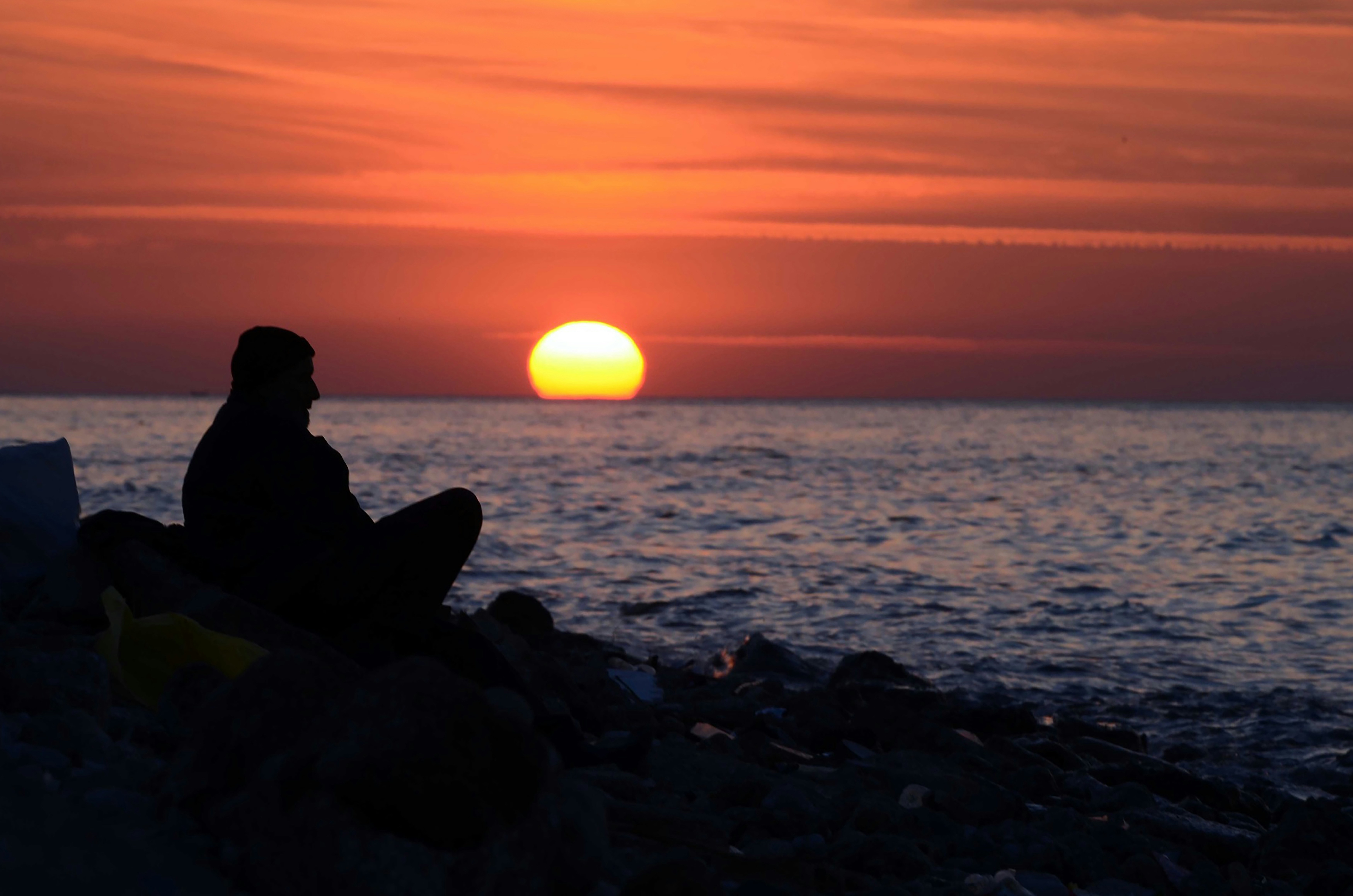 A person sitting on a beach watching the sun set photo – Free Sunset ...