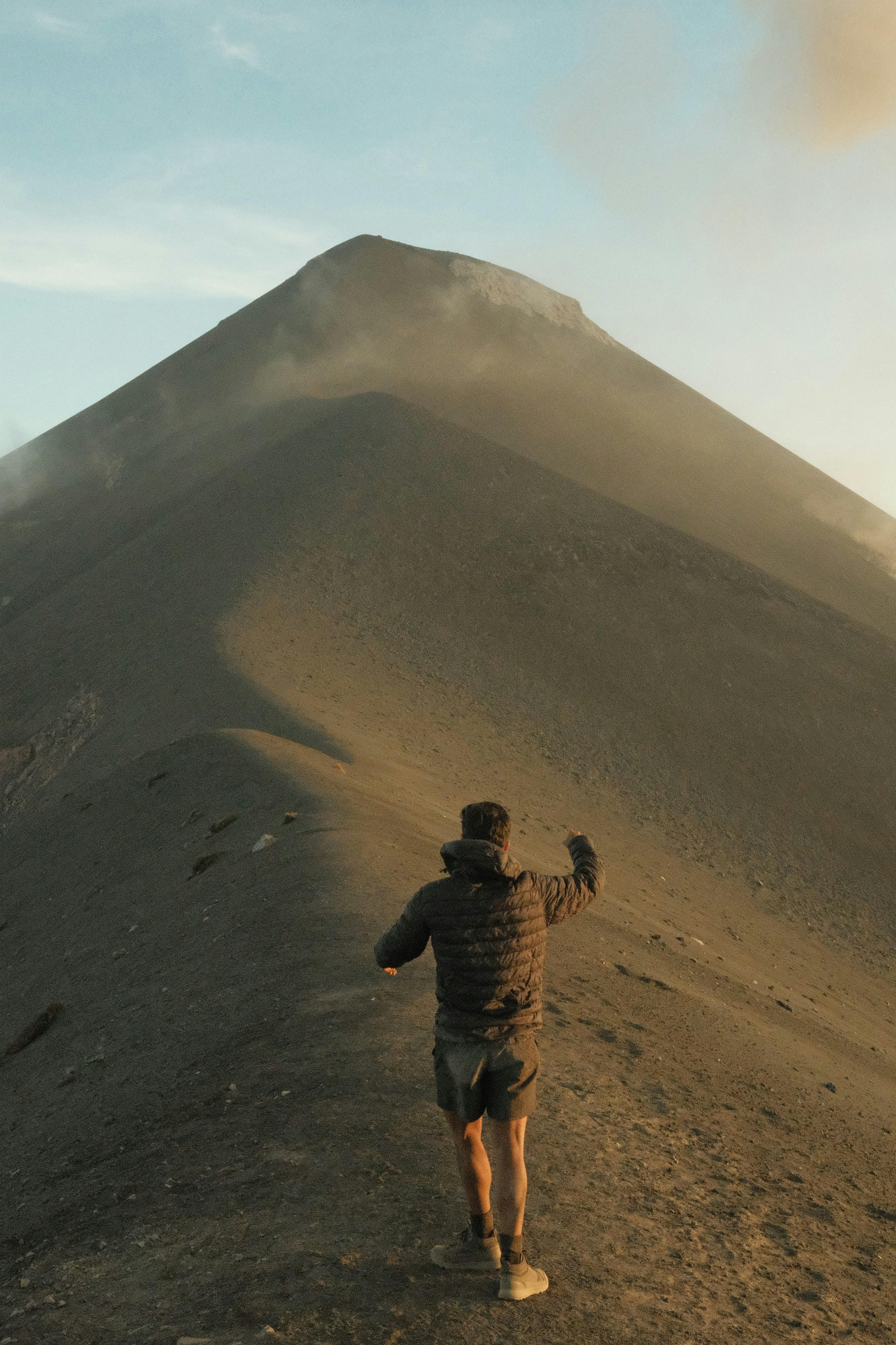 Person walking along the narrow ridge of a volcano under a clear sky.