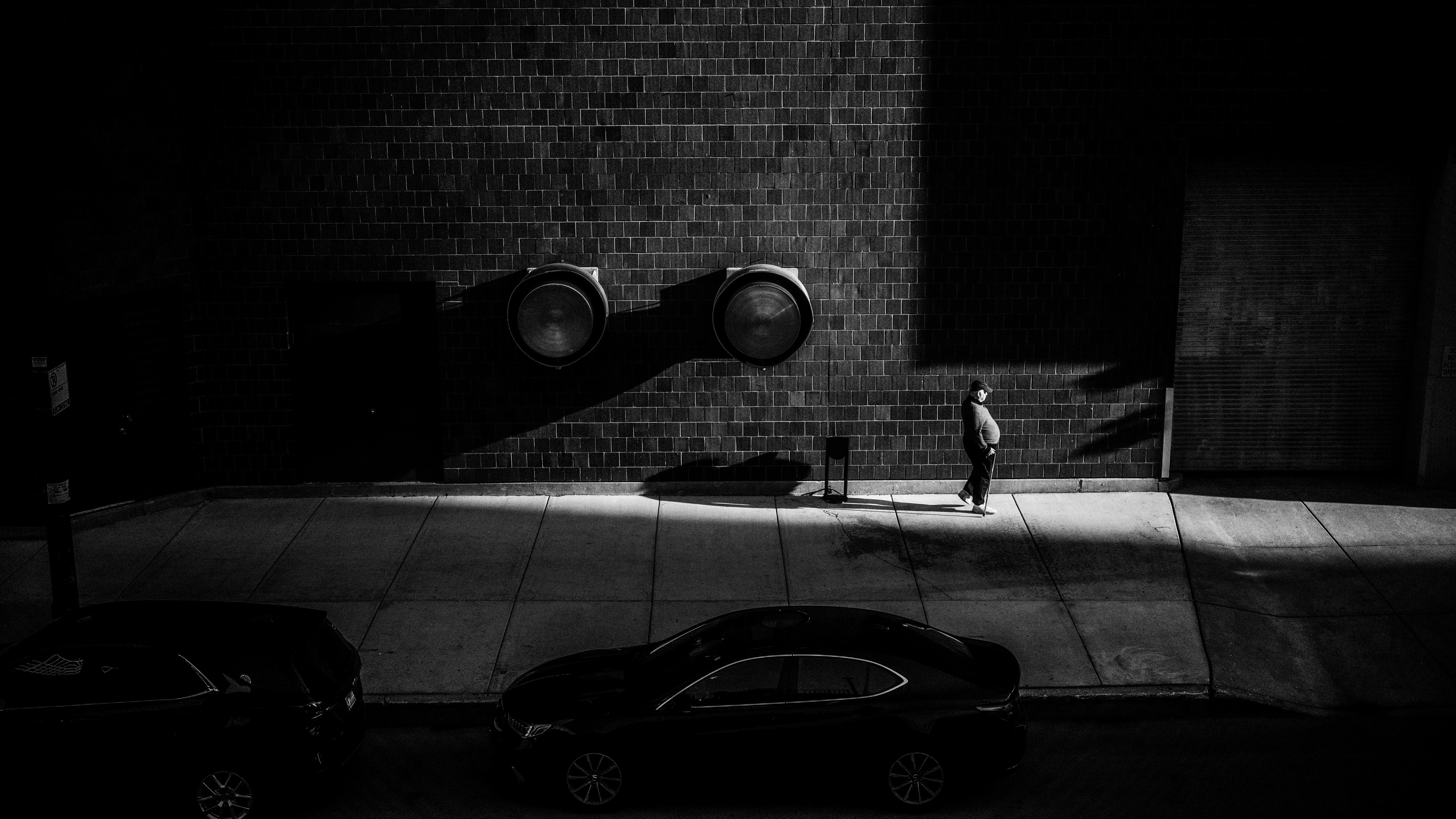 Man walking in beam of light against brick wall. | a black and white photo of a person standing in front of a brick wall