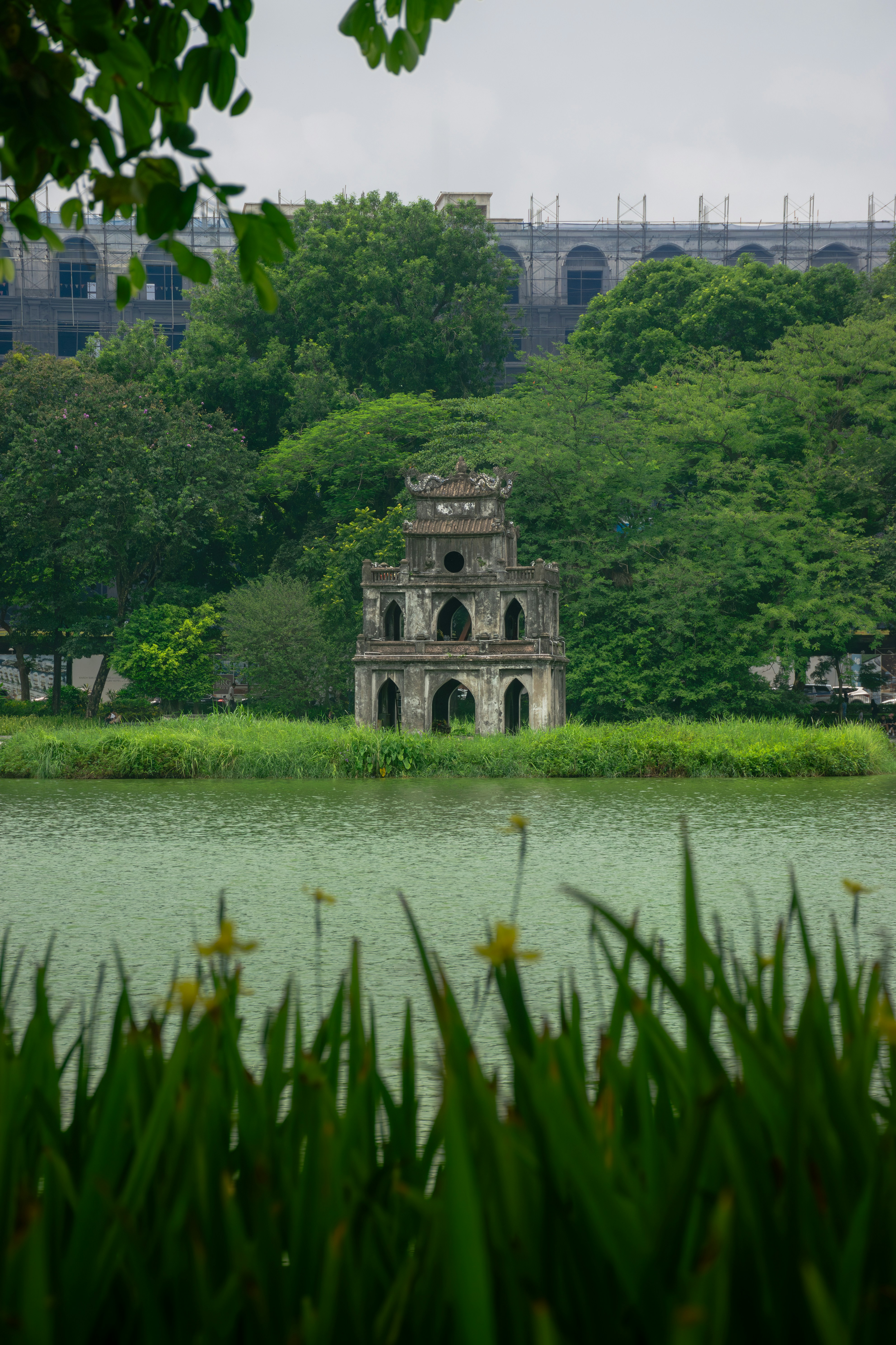 Turtle Tower stands majestically on an island, framed by lush greenery and reflective waters, embodying the essence of Hanoi's cultural heritage.